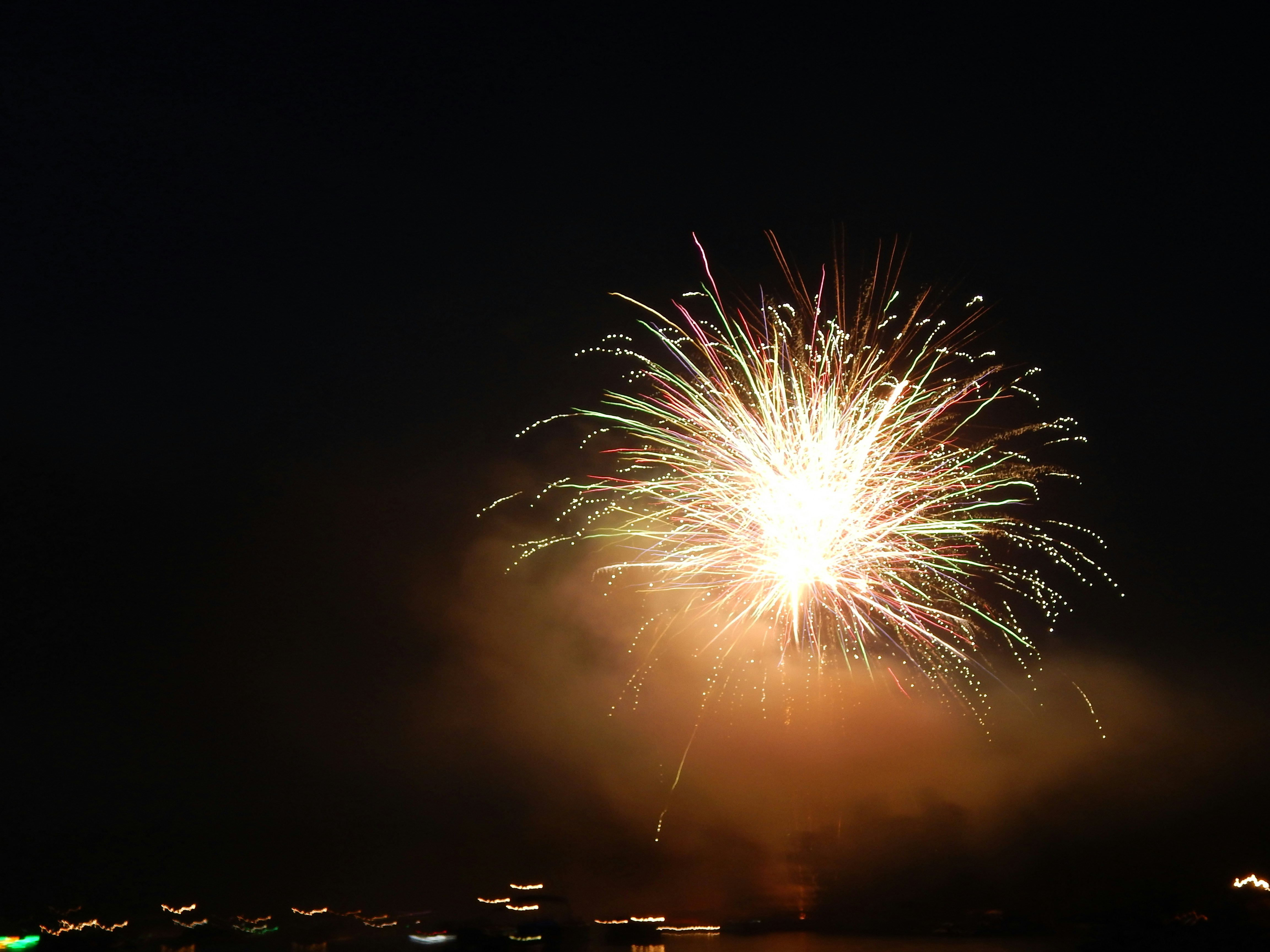 Colorful fireworks bursting in the night sky, illuminating the surrounding darkness with vibrant trails. Smoke adds depth to the festive atmosphere.