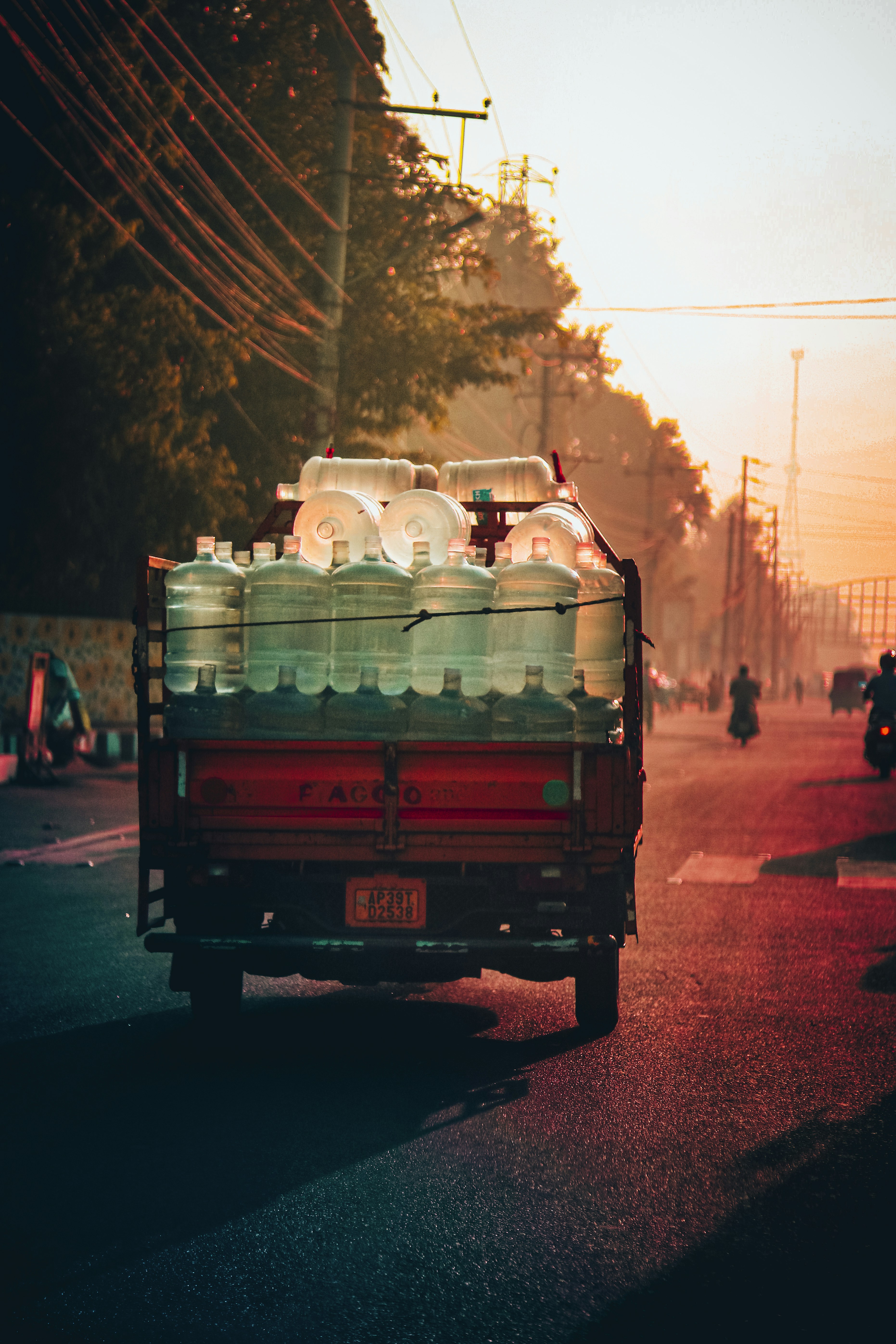 A truck loaded with clear water bottles navigates a sunlit street, highlighting urban life and essential services.
