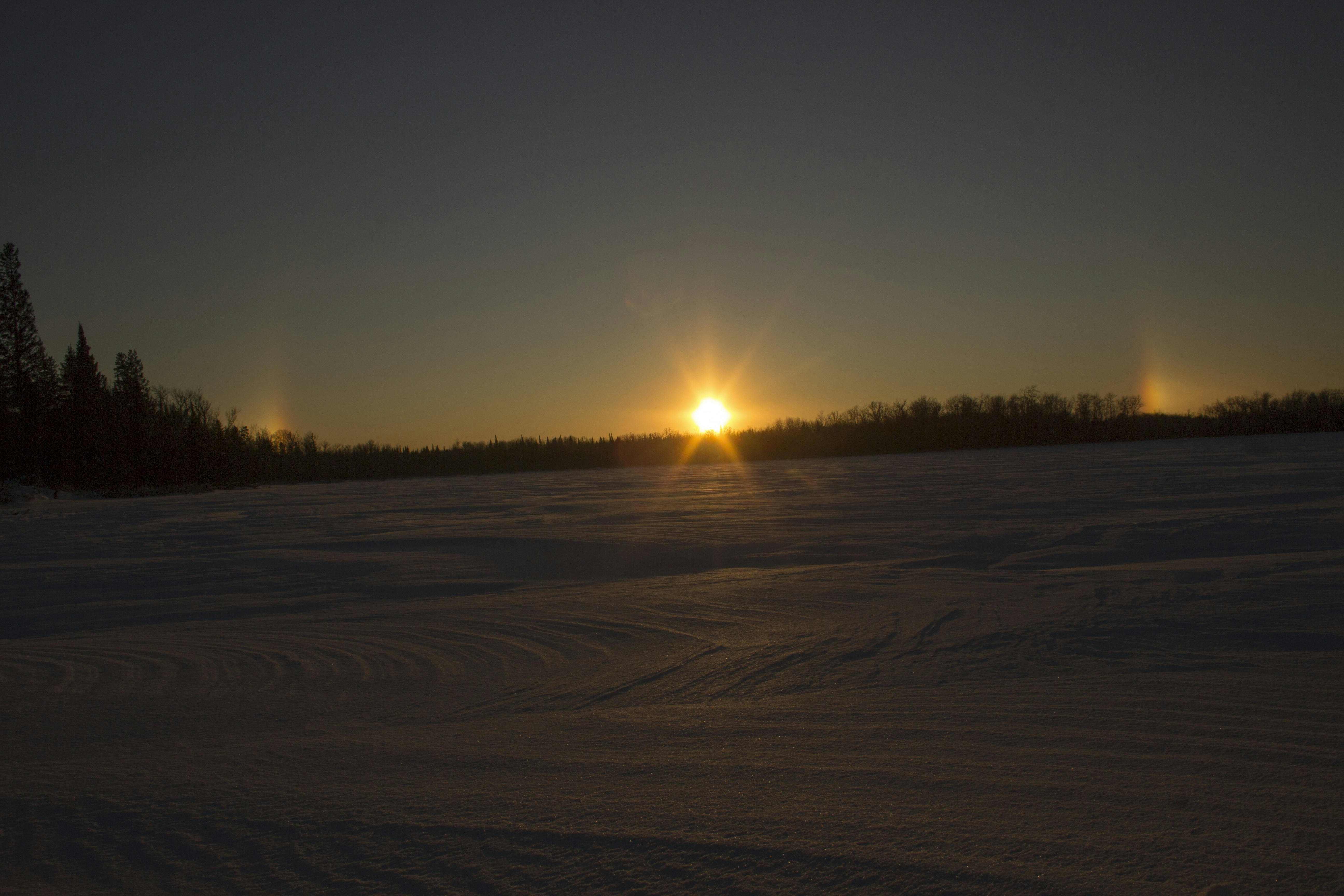 Frigid temperatures and ice crystals in the air create rainbows on each side of the sun called sundogs. An artistic landscape-snow-scape on a lake from heavily packed wind blown snow. Drifts and frozen ripples and waves are a wonder to behold if one does not mind frosty eyelashes and cold biting through the warmest parka