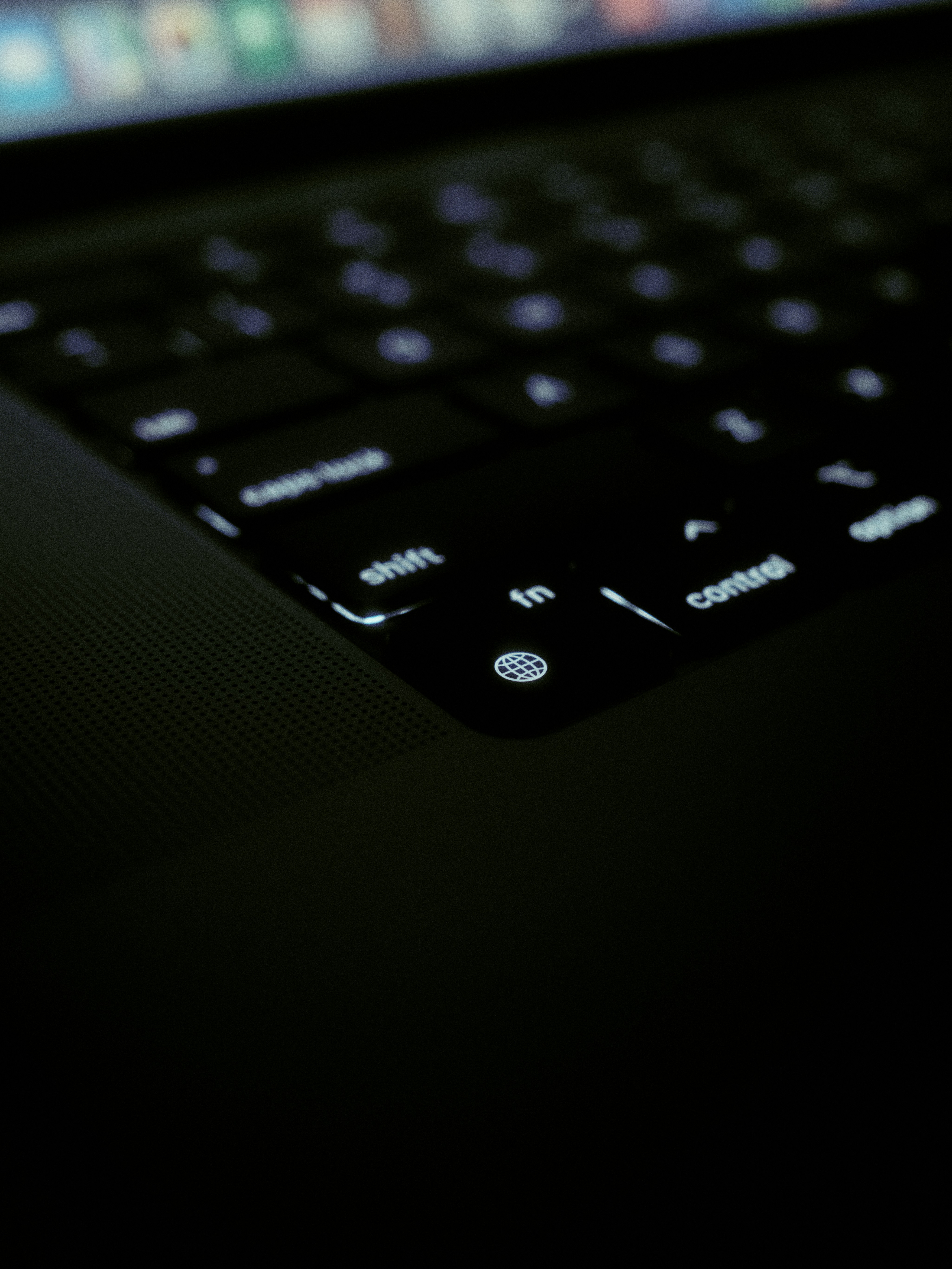 Close-up of a backlit keyboard showcasing the 'fn' key and an illuminated globe icon, set against a dark background.