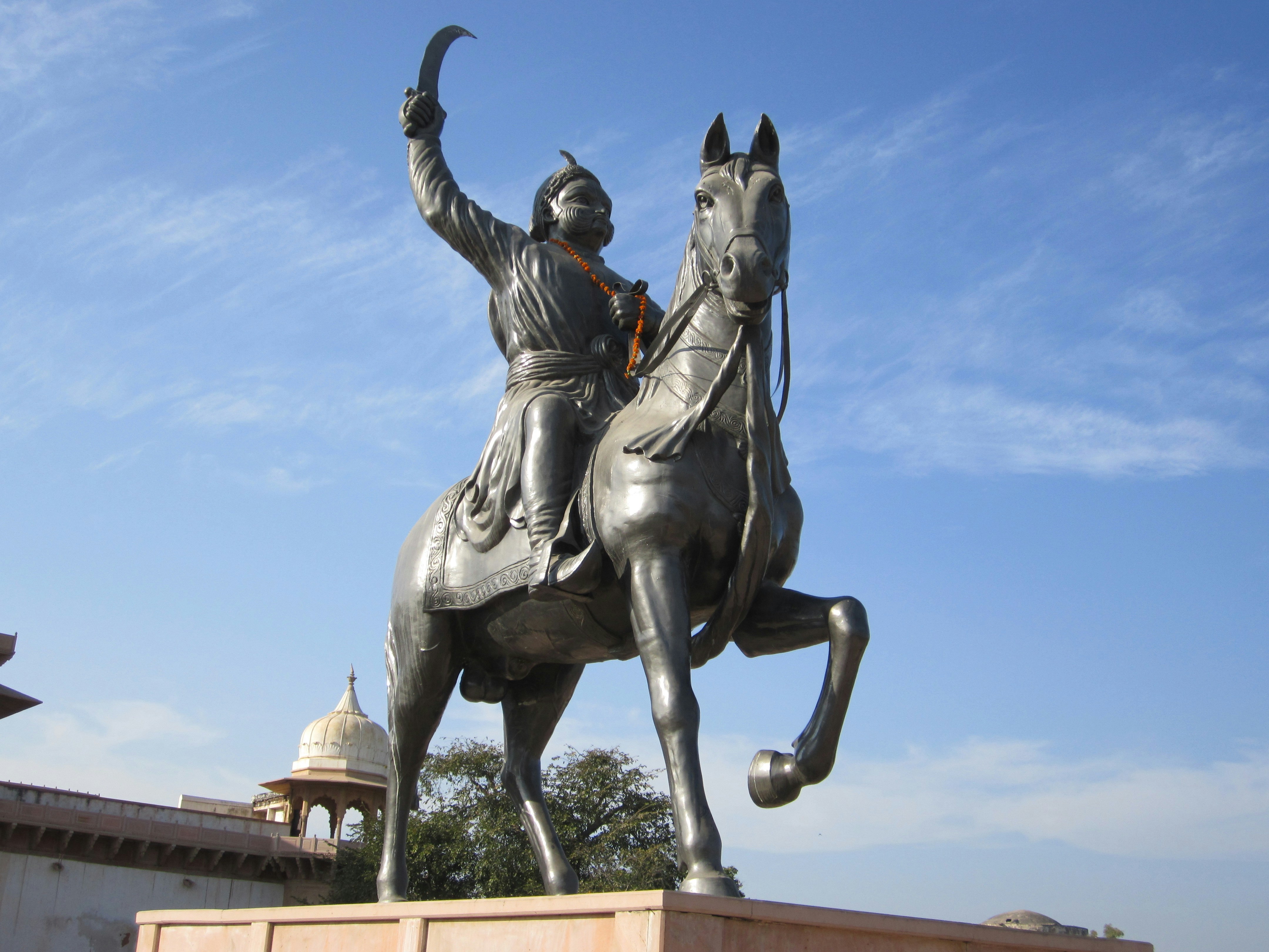 Bronze equestrian statue of a knight raising a curved sword, mounted on a pedestal against a bright blue sky.
