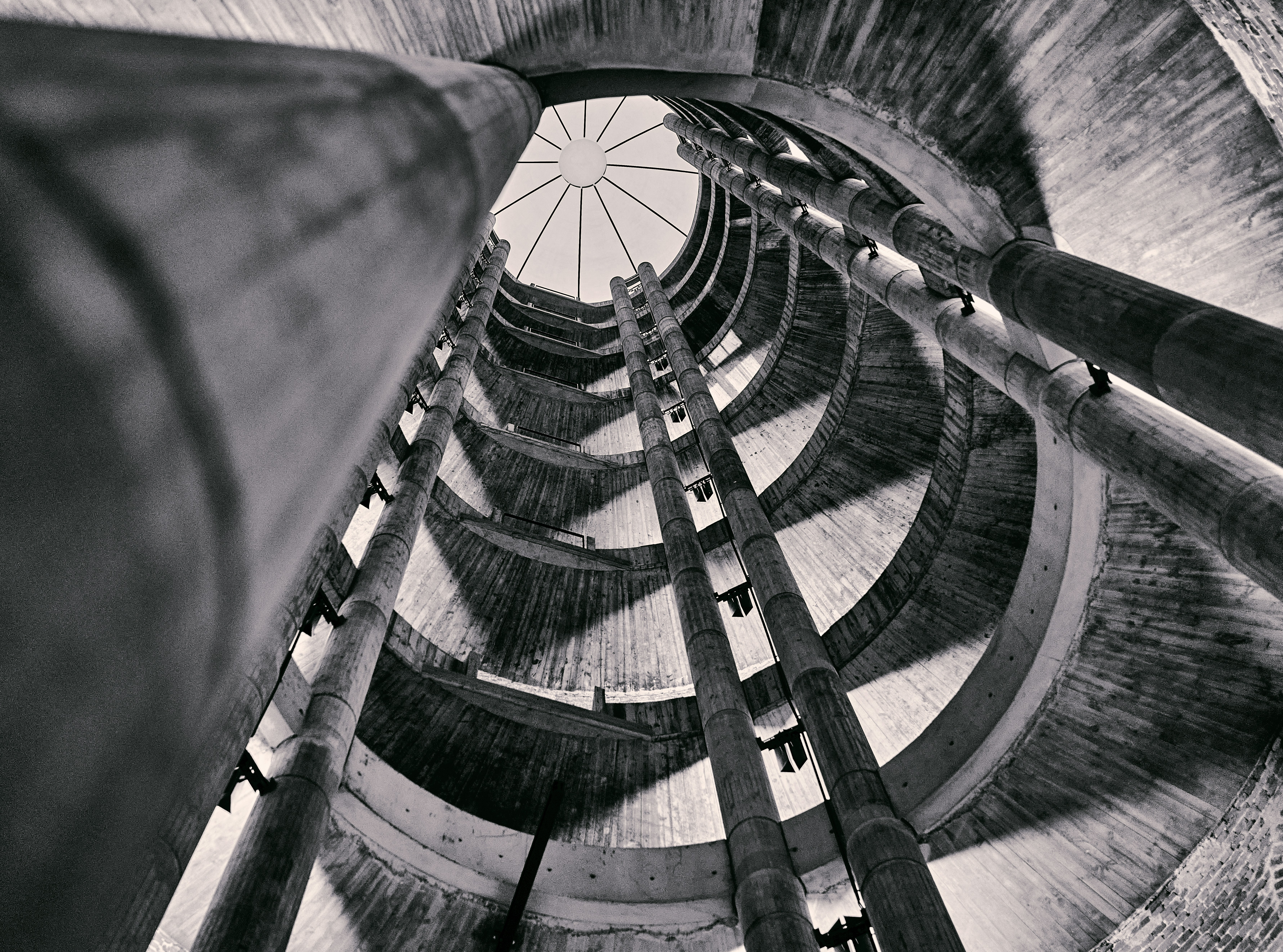 Abstract architectural view from the ground up, showcasing a spiral structure with towering concrete columns and a circular skylight.