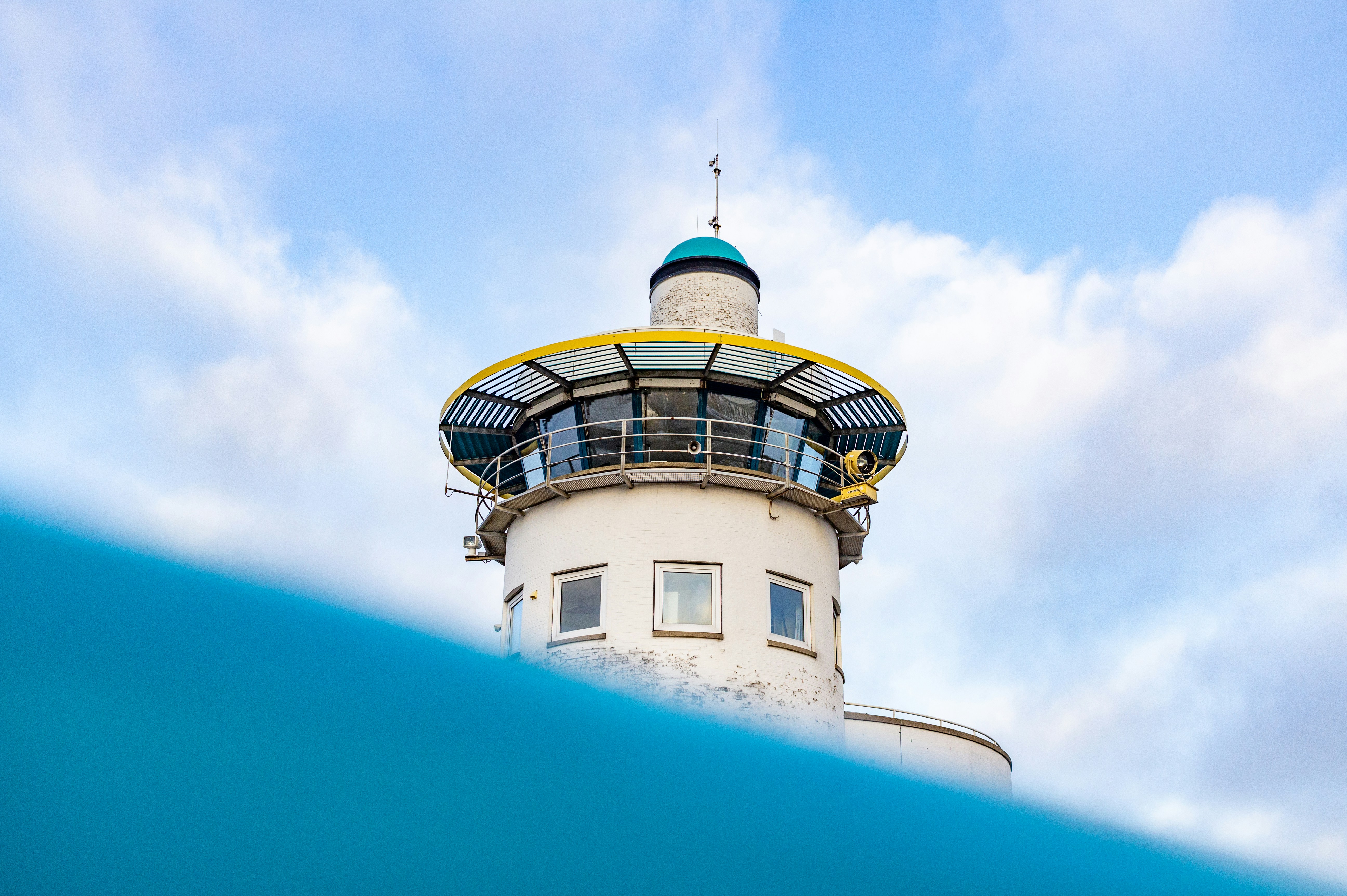 White lighthouse tower with a blue sky, partially obscured by a turquoise foreground element.