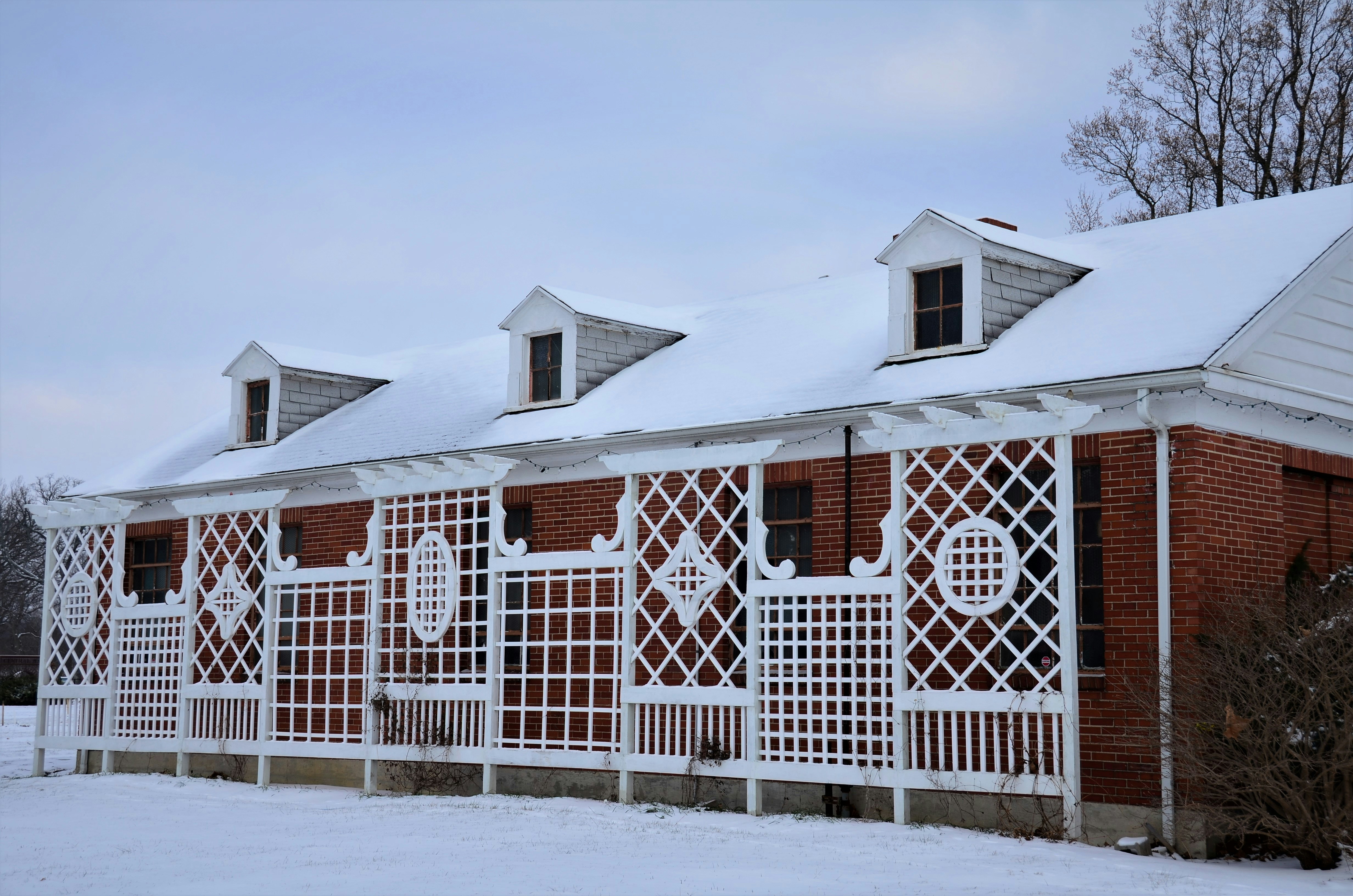 A charming brick structure adorned with intricate white latticework, blanketed in fresh snow under a soft winter sky.
