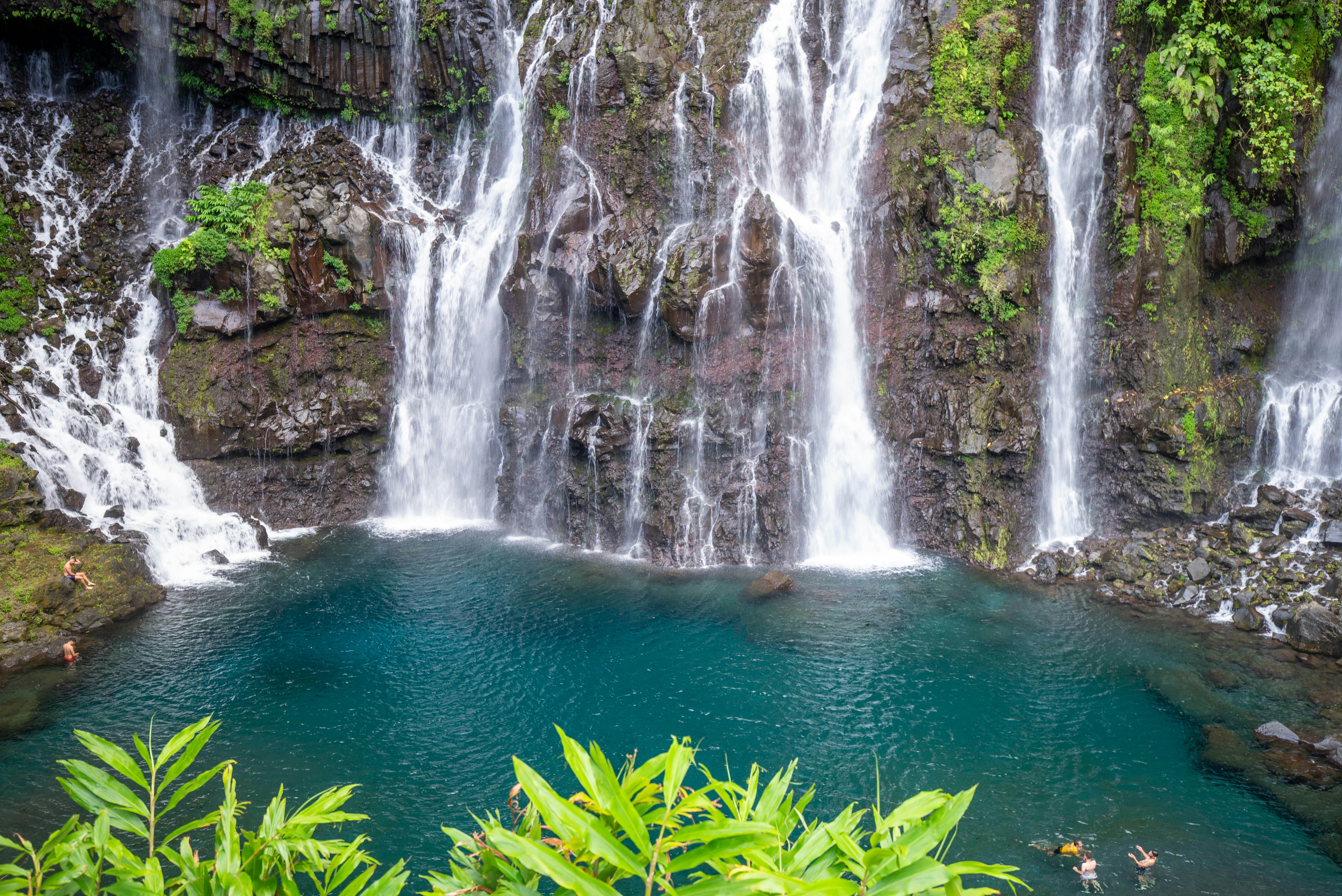 Swimmers enjoying a serene pool beneath cascading waterfalls surrounded by lush greenery.