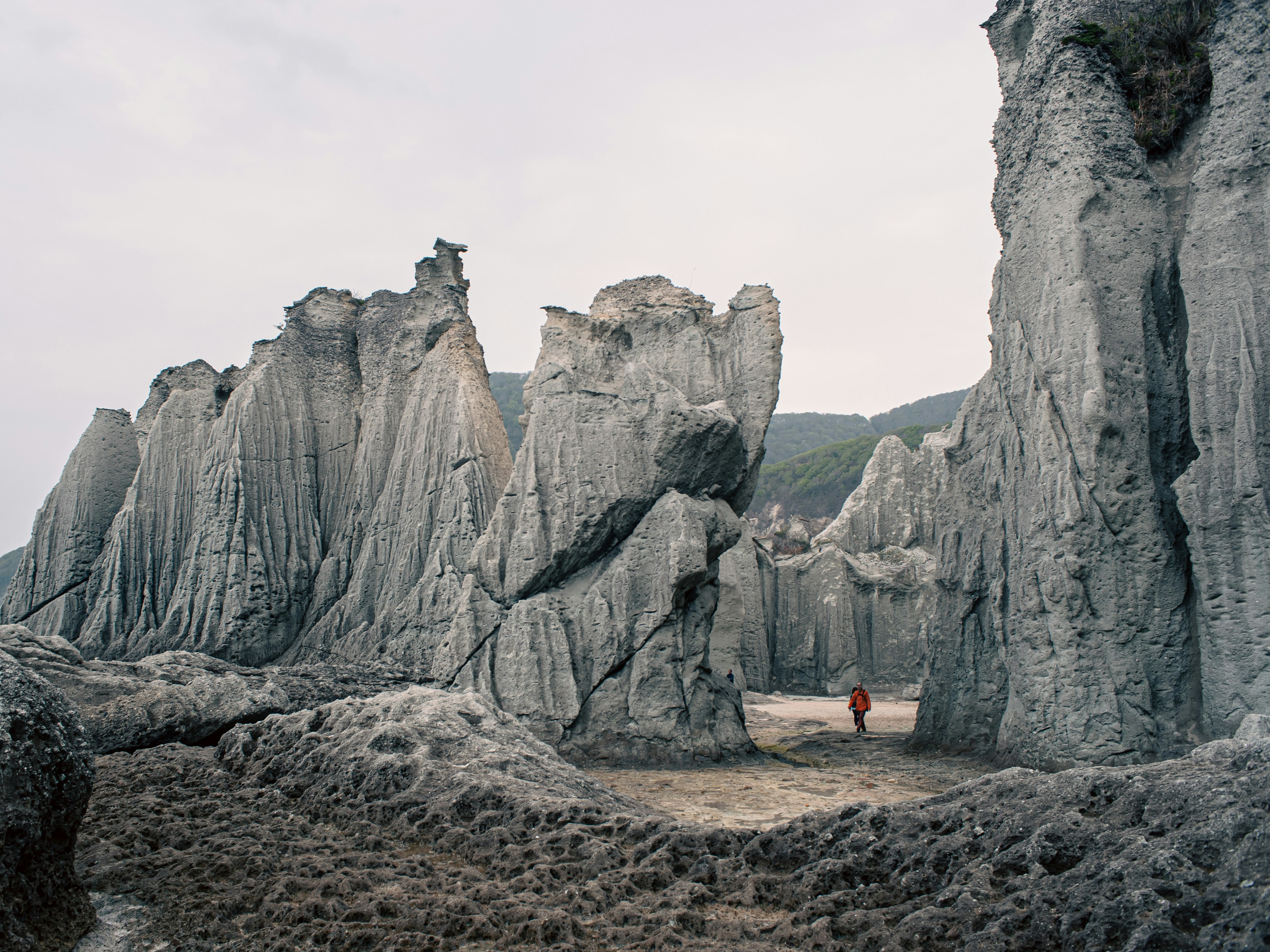 A lone figure in a red jacket traverses a surreal landscape of towering rock formations, showcasing nature's sculptural artistry. The scene evokes a sense of exploration and wonder.