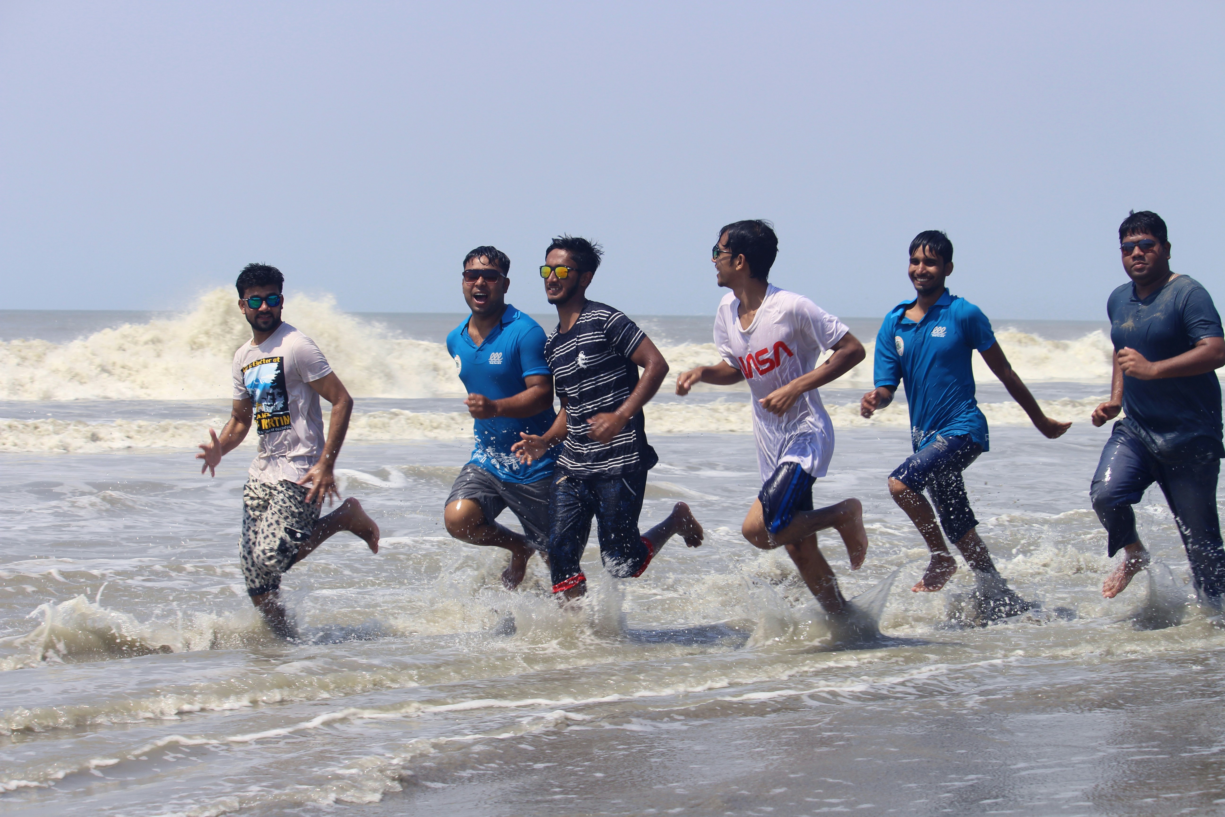 A group of men run through the water at the beach photo – Free ...