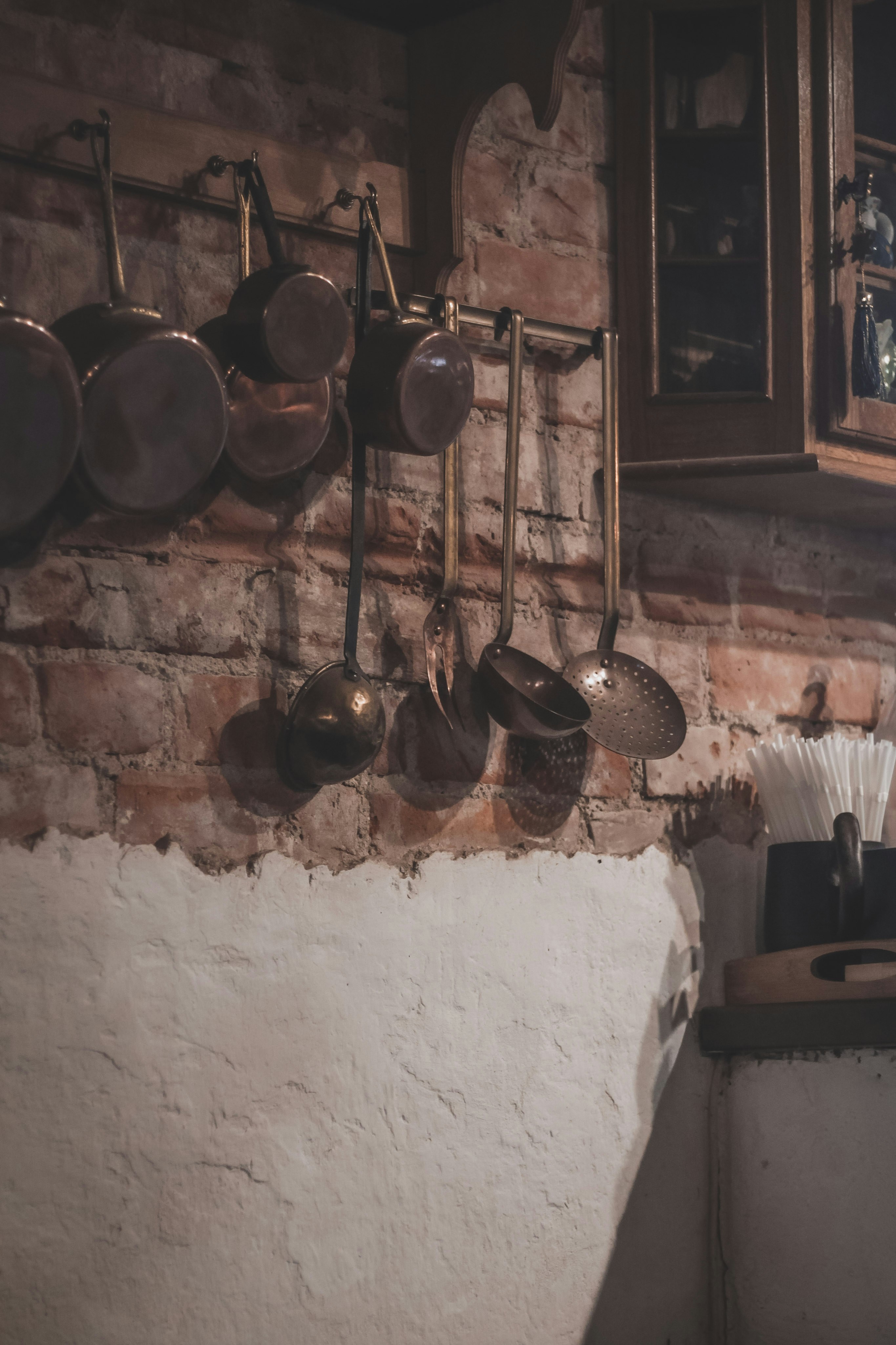 Hanging copper pots and utensils adorn a rustic brick kitchen wall.