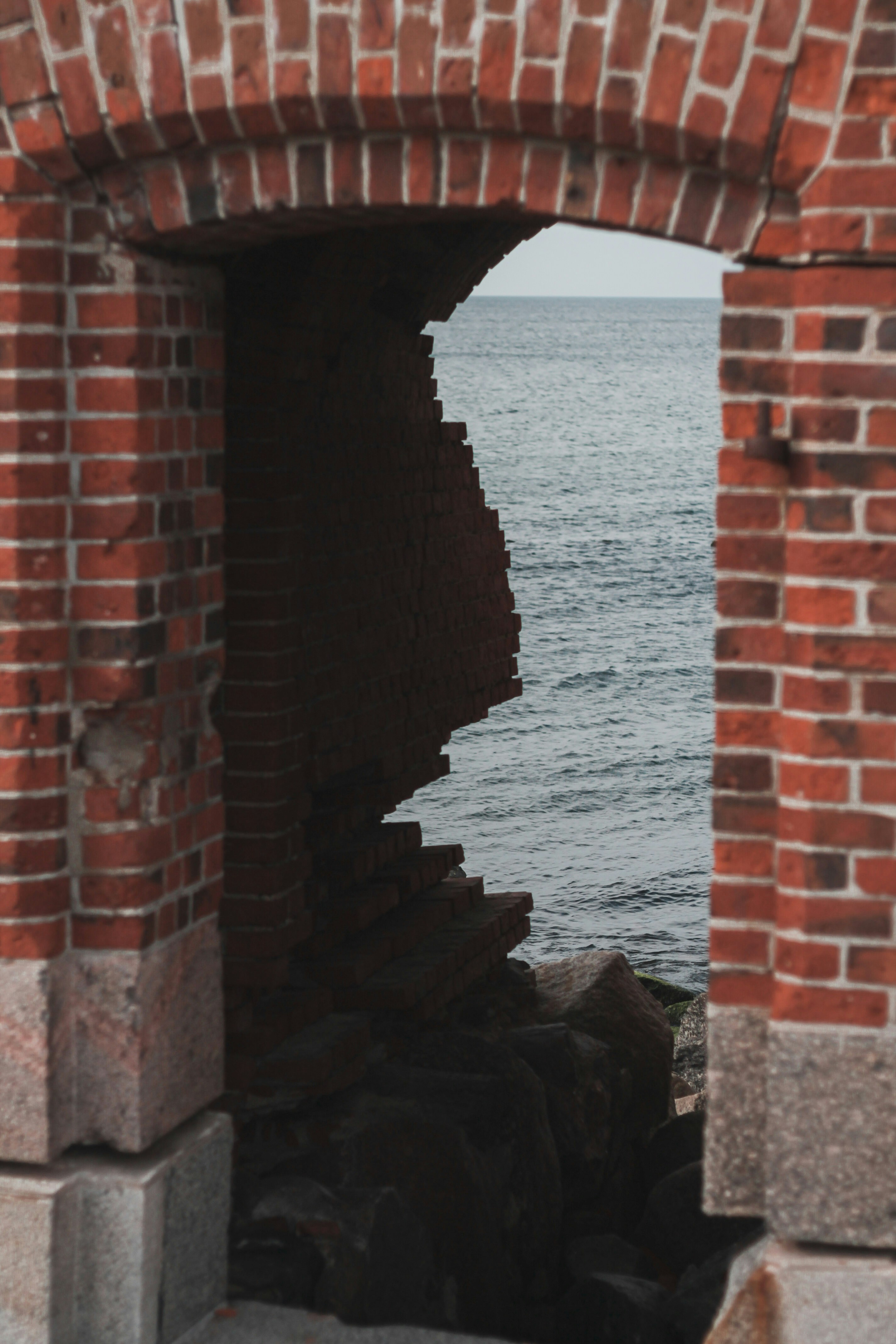 Fragmented brick archway revealing a serene view of the ocean beyond, highlighting the contrast between man-made structures and nature's expanse.
