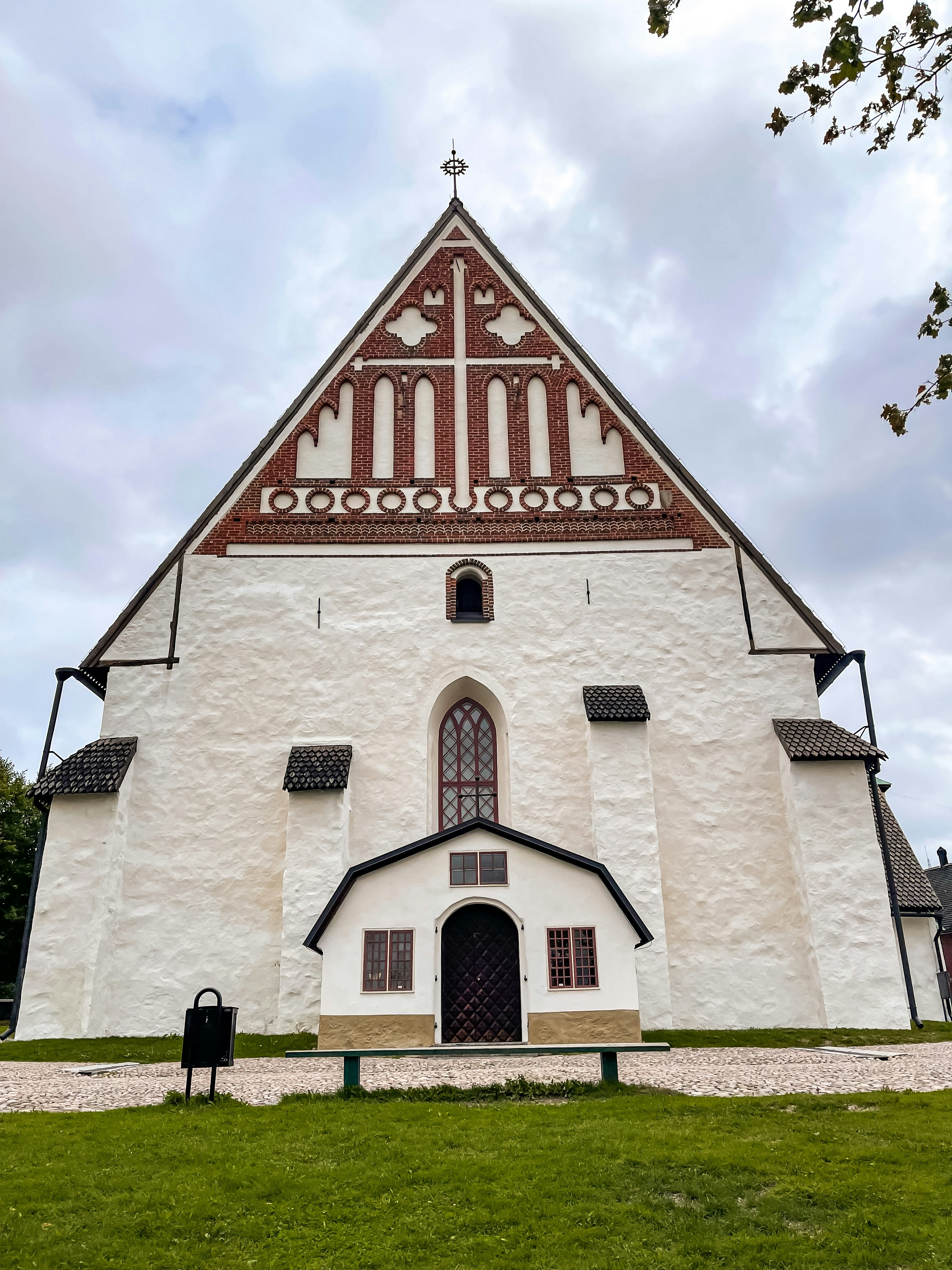 Historic church with a striking gabled roof and intricate brickwork, framed by lush greenery and a serene sky.