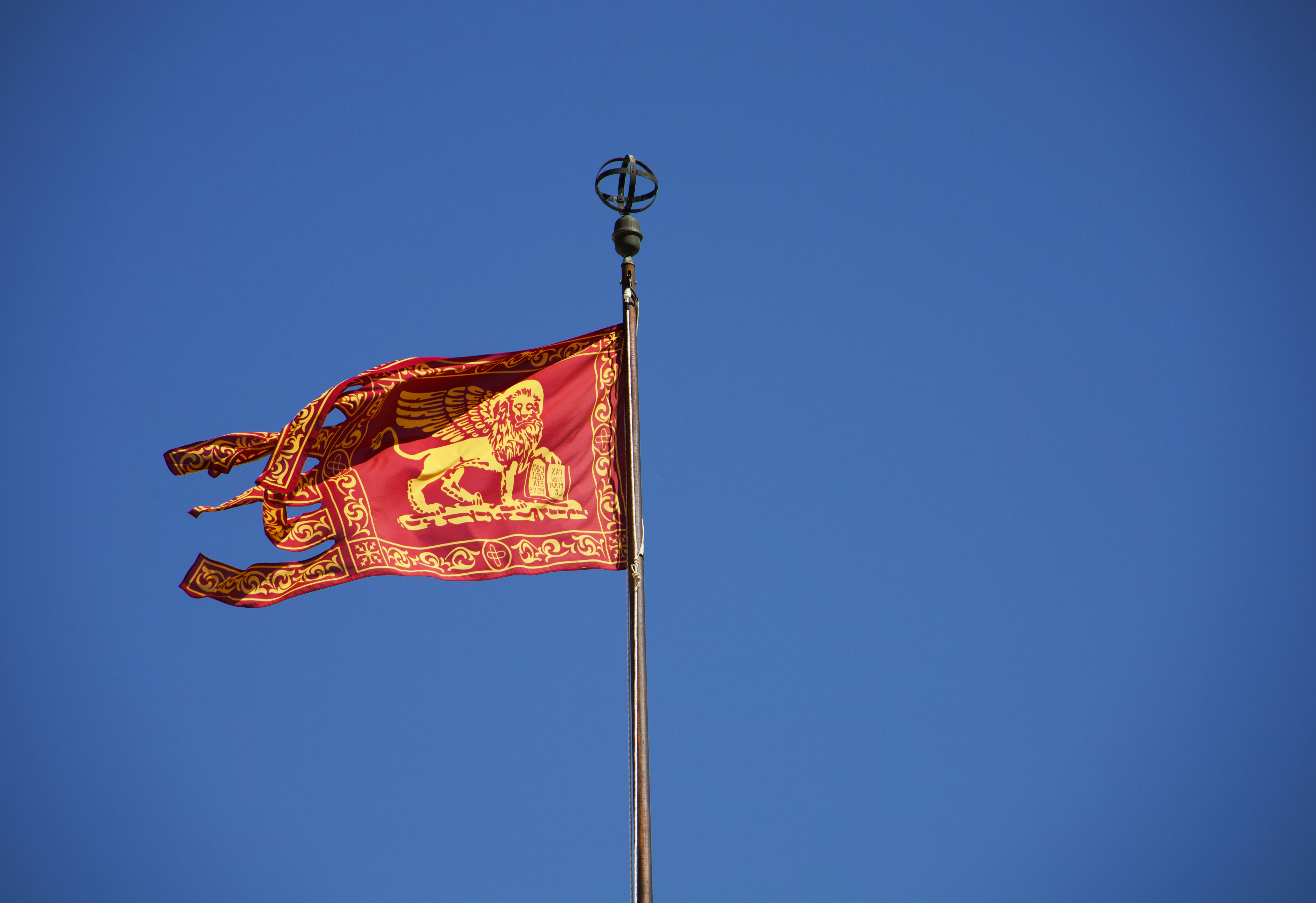 A red and gold flag flying in the wind photo – Free Venecia Image on ...
