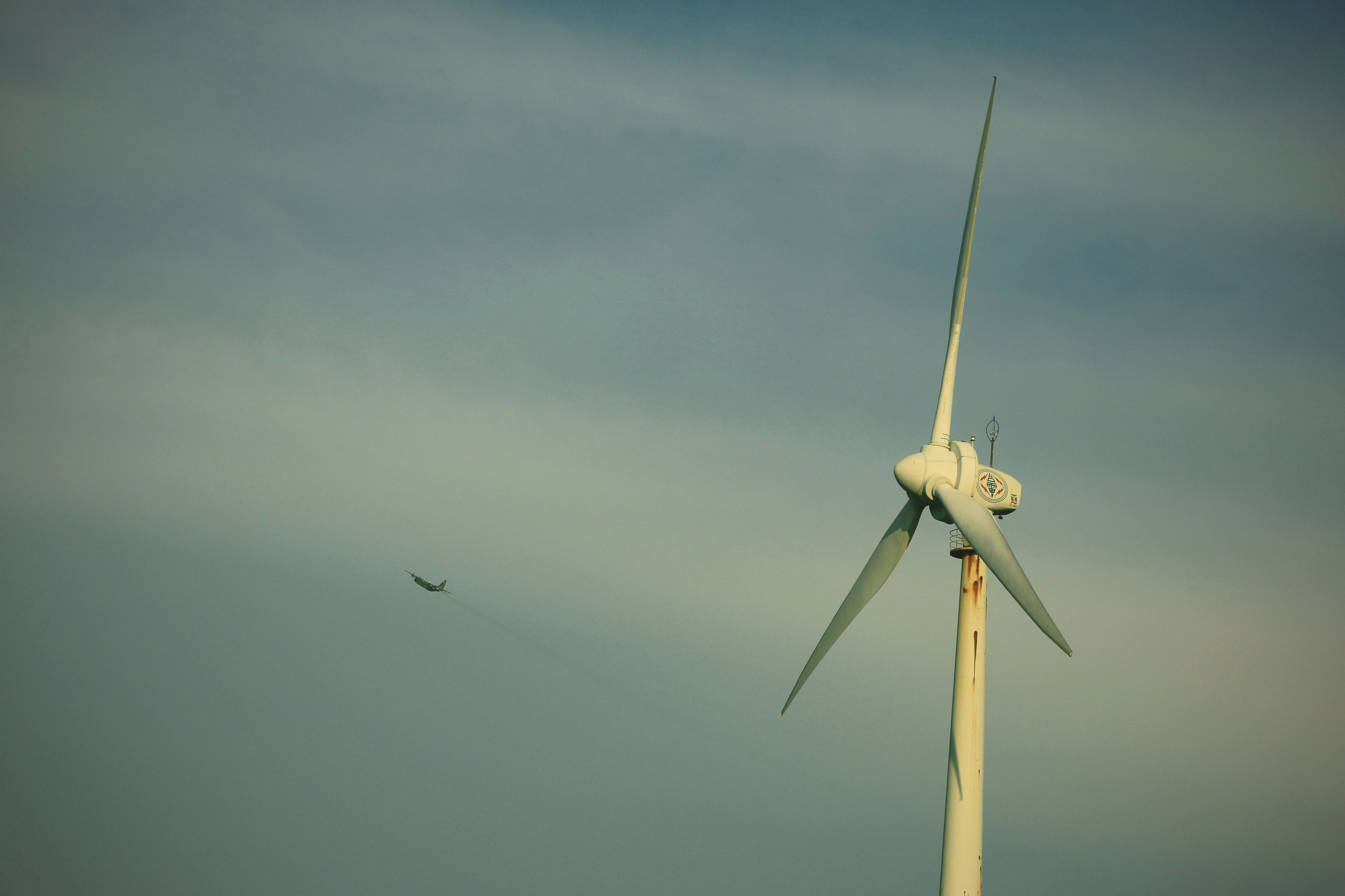 A wind turbine and a plane flying in the sky photo – Free Penghu Image ...