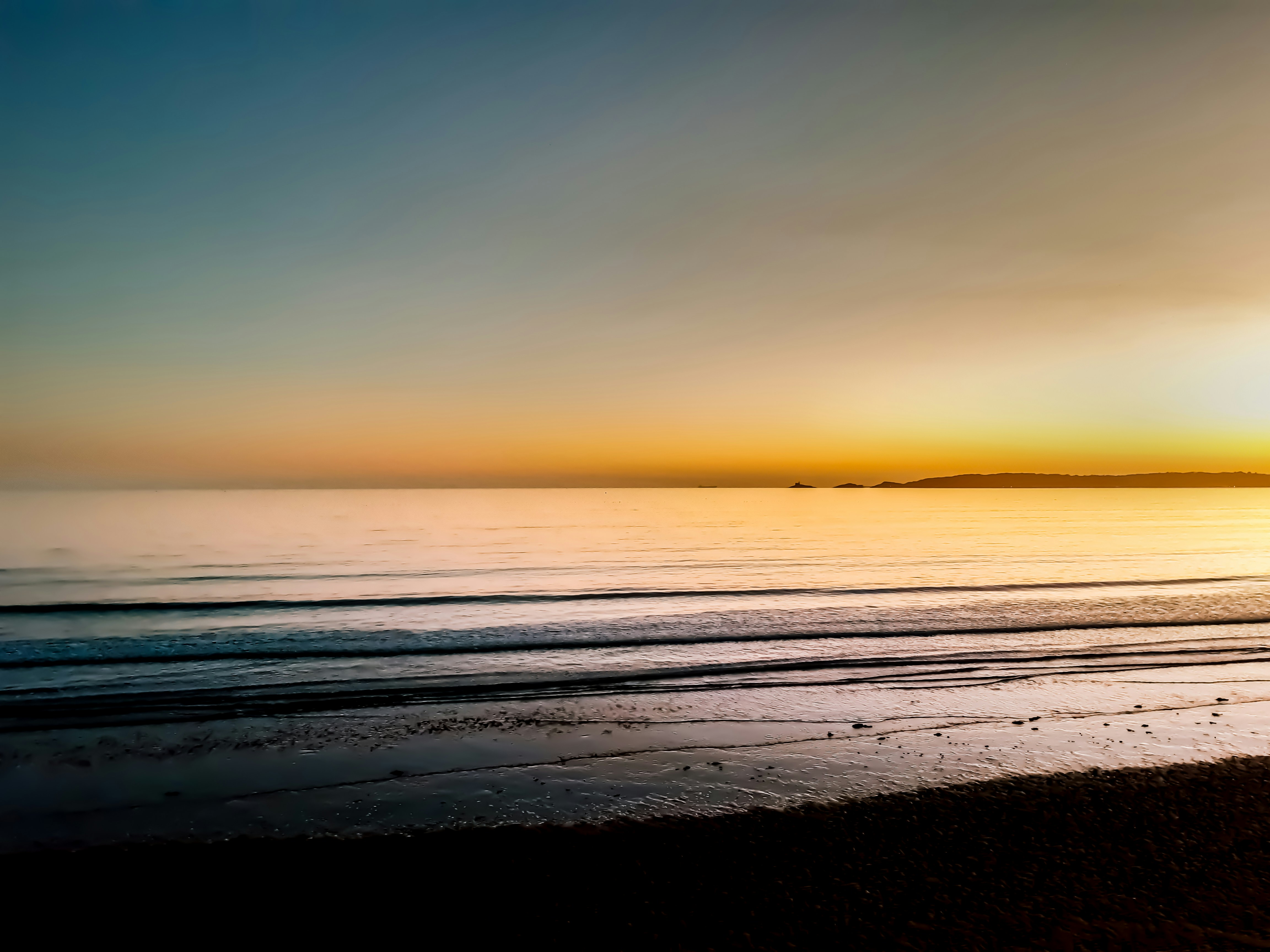 Sunset over a calm ocean with gentle waves and a gradient sky.