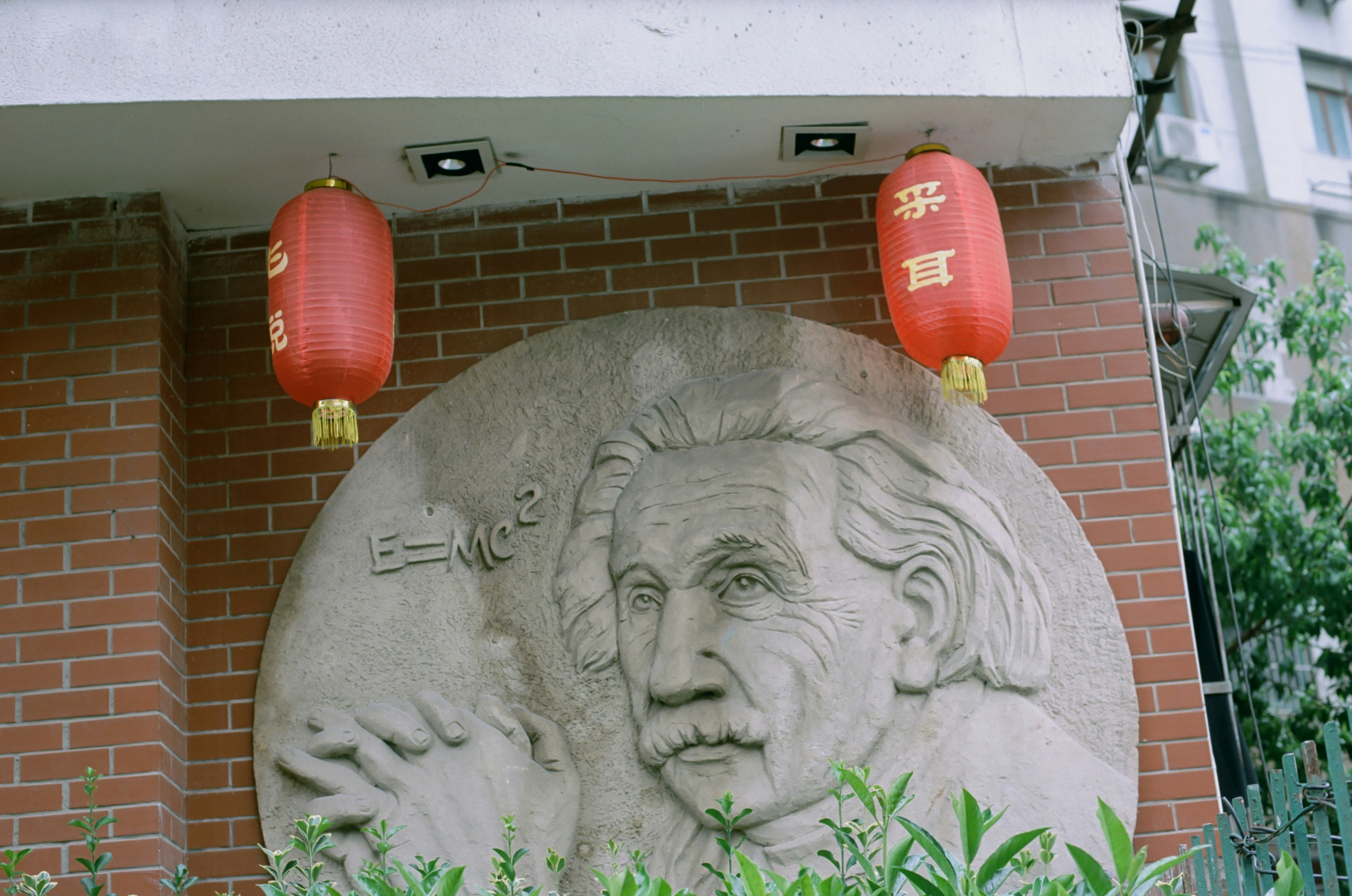 Relief sculpture of Albert Einstein with his famous equation, framed by traditional Chinese lanterns and greenery.