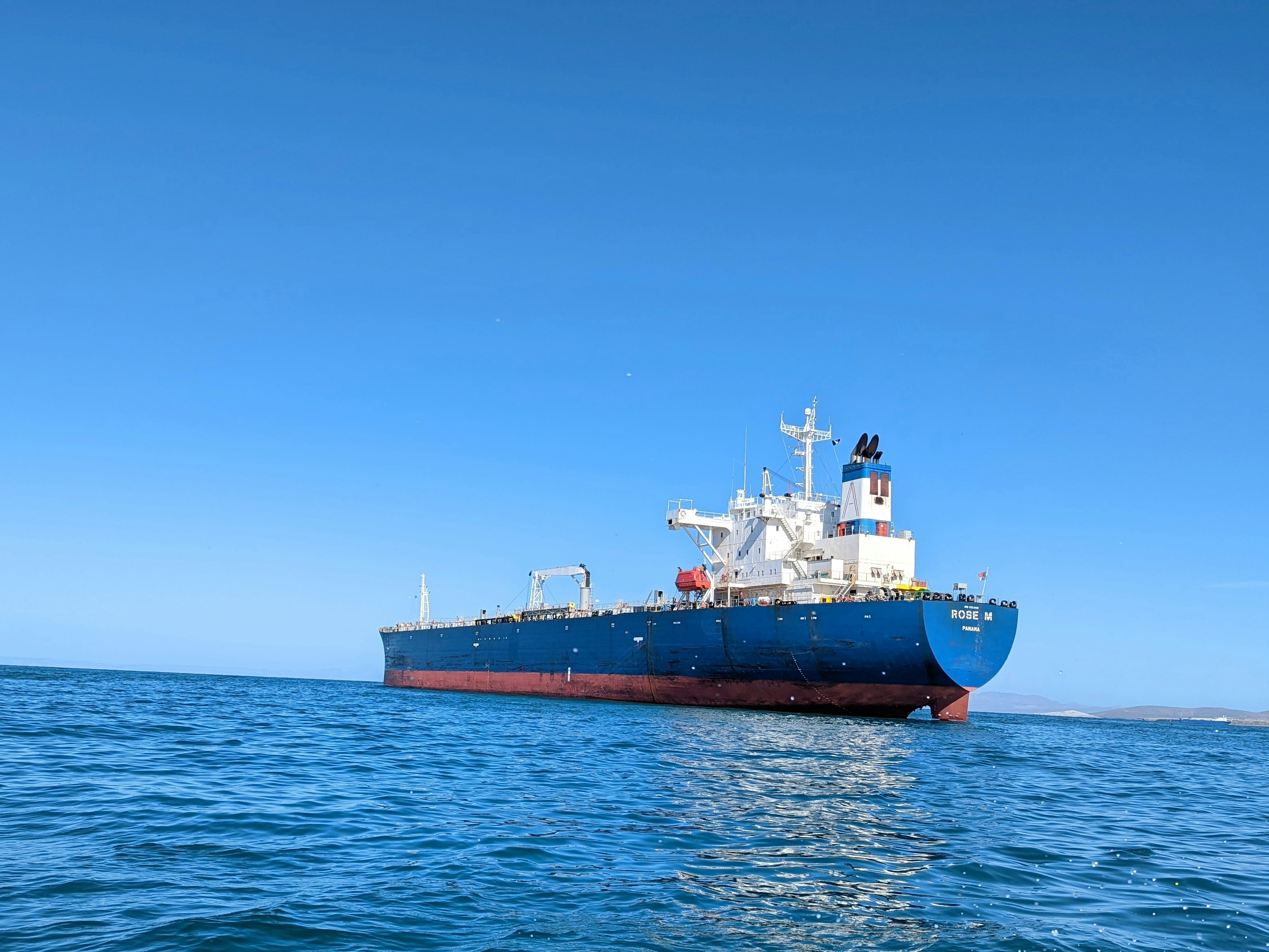 Cargo ship sailing under a clear blue sky in calm waters.