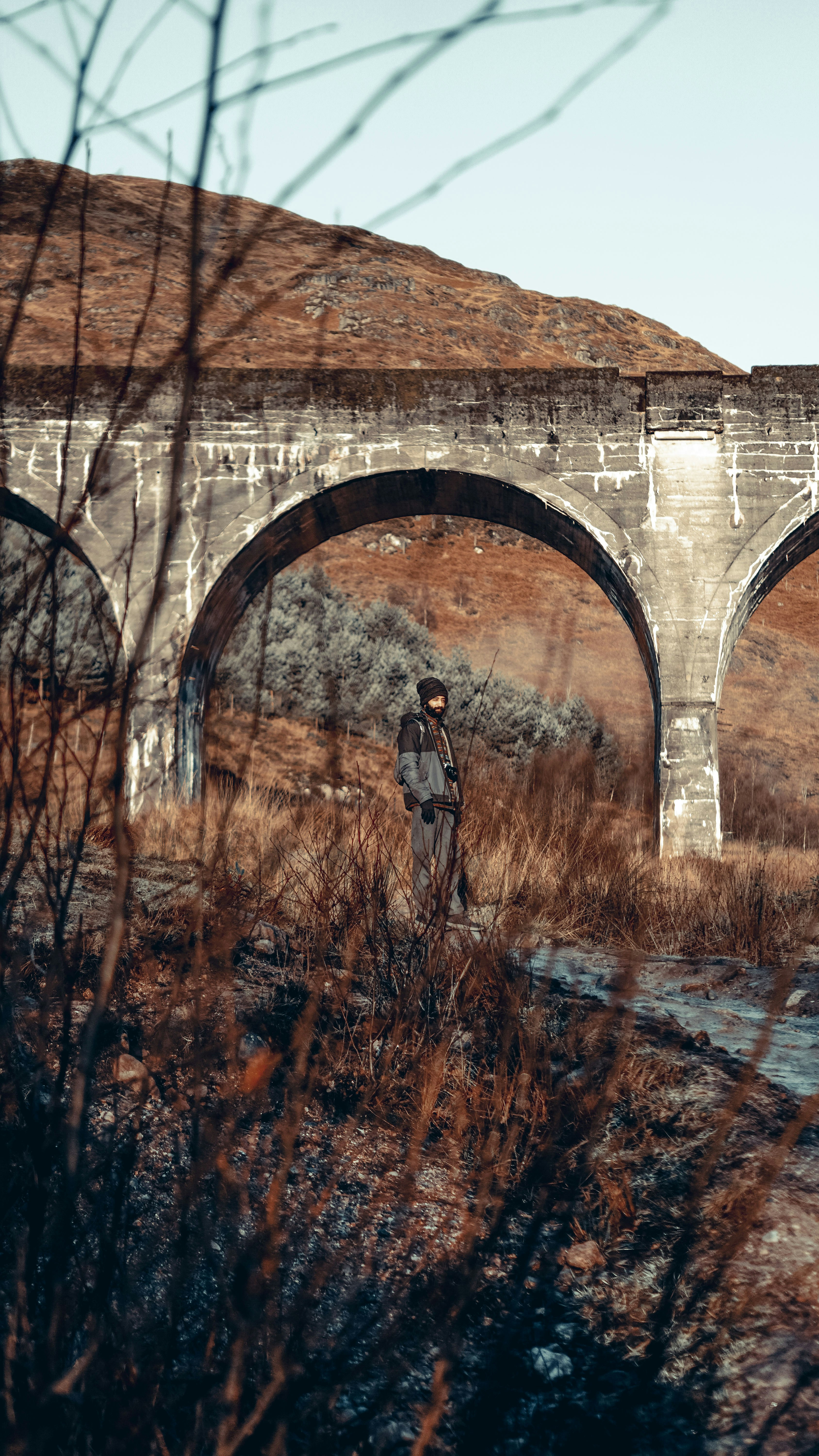 a man standing in front of a stone bridge