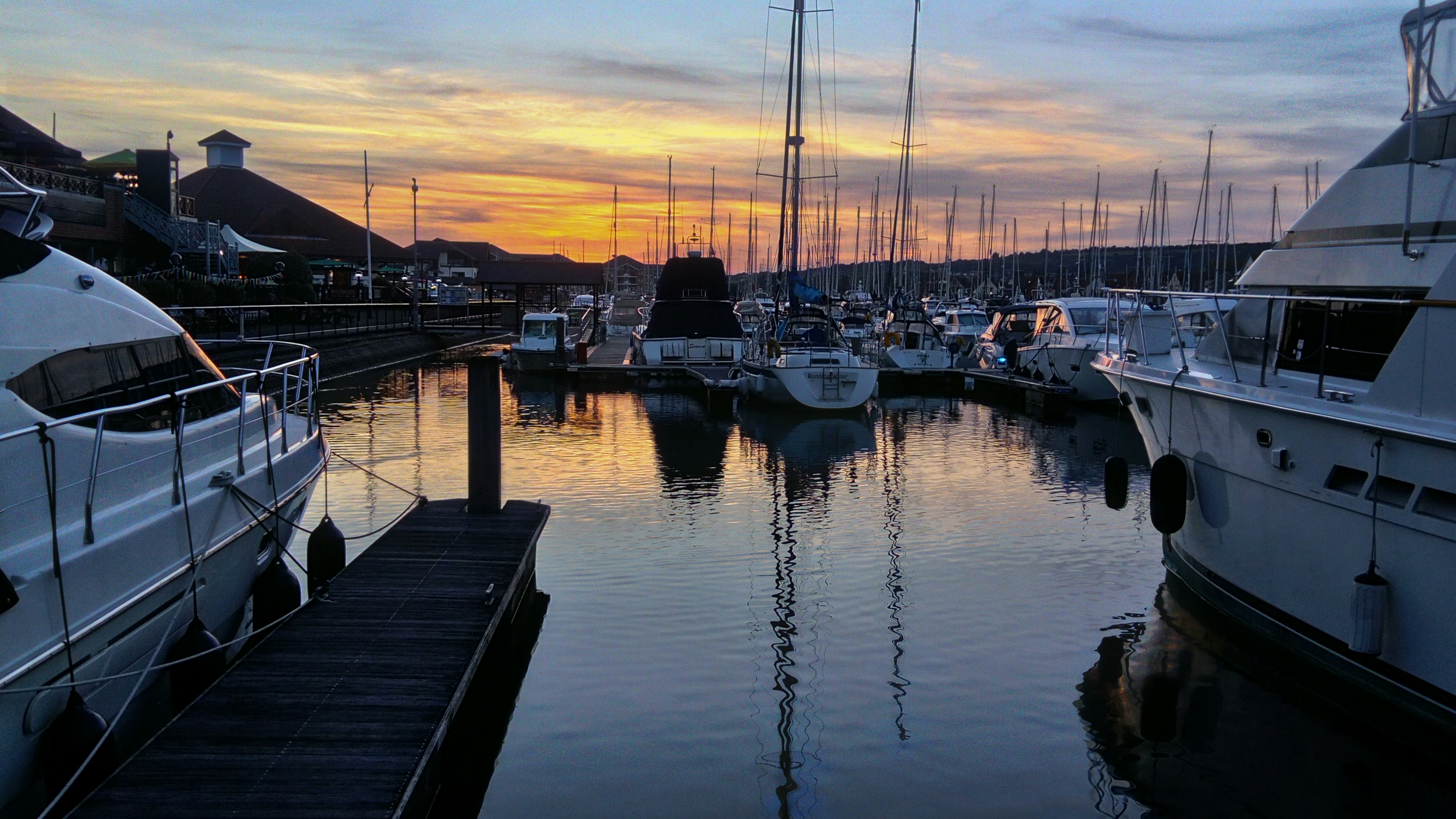 White boats docked in a marina at sunset, with vibrant colors reflecting on calm waters.