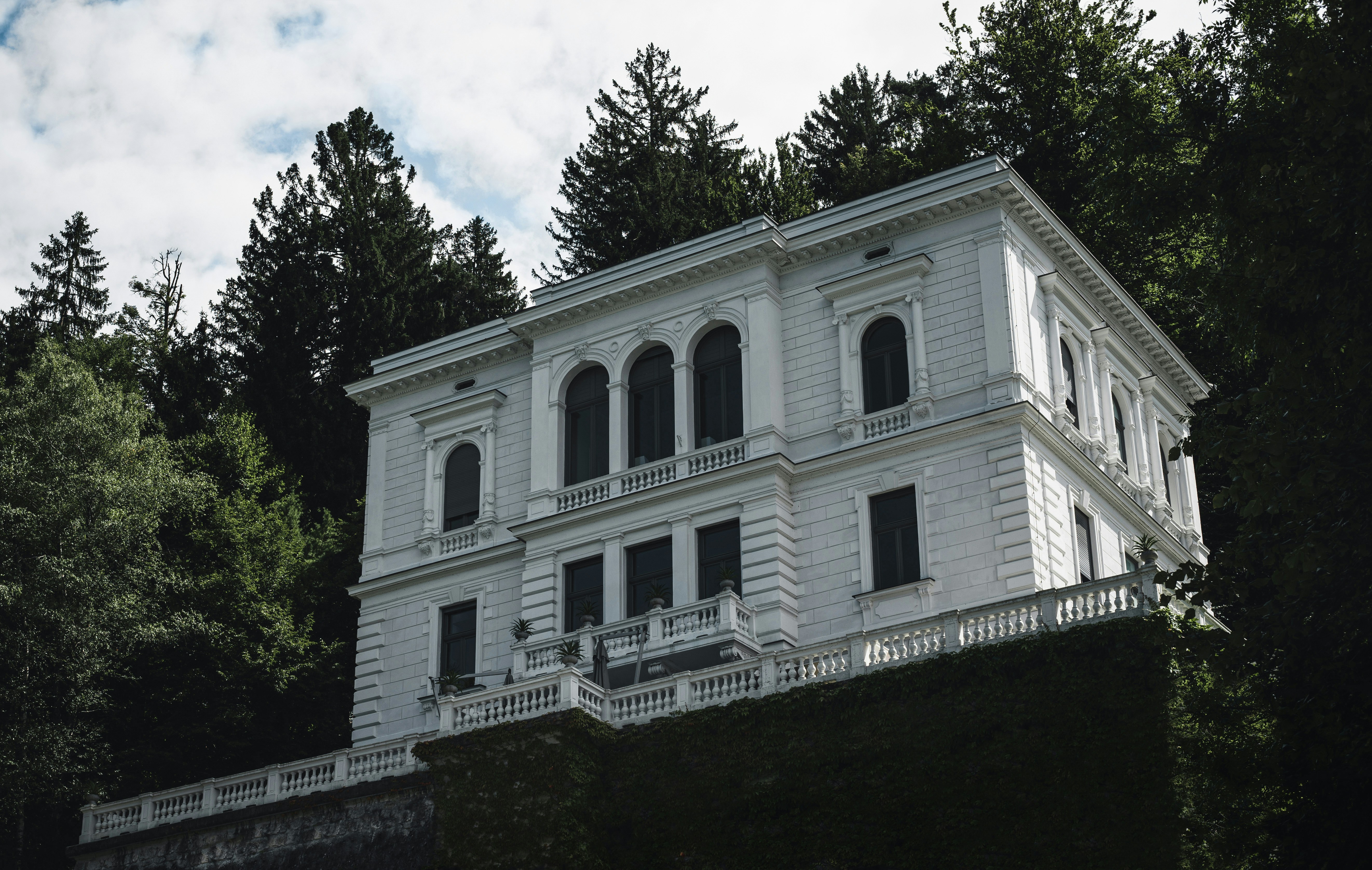 Elegant white mansion perched on a green hillside surrounded by dense forest.