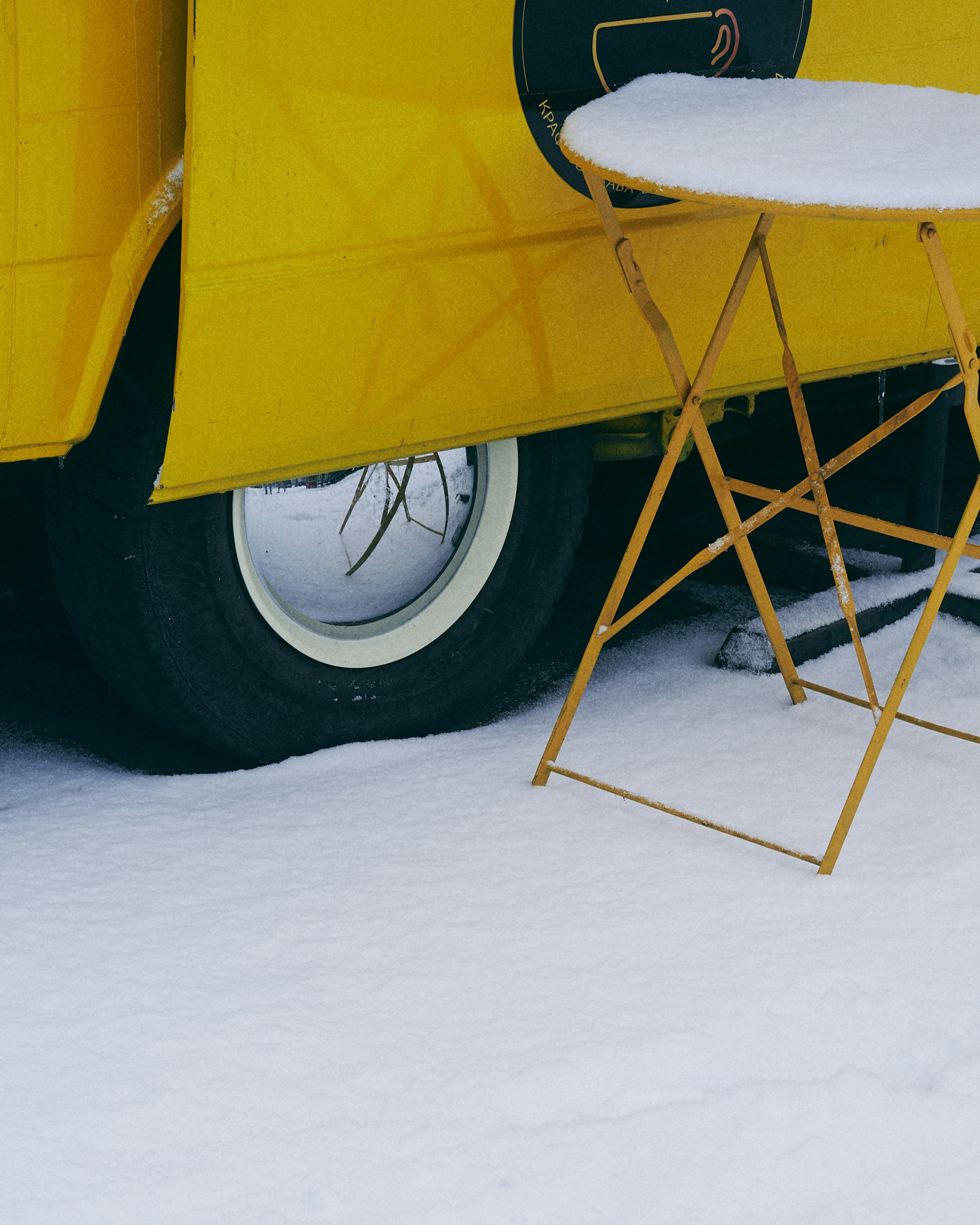 Yellow Vintage Van in Winter Quiet: Snow, Wheel, and Folded Chair as a Pause