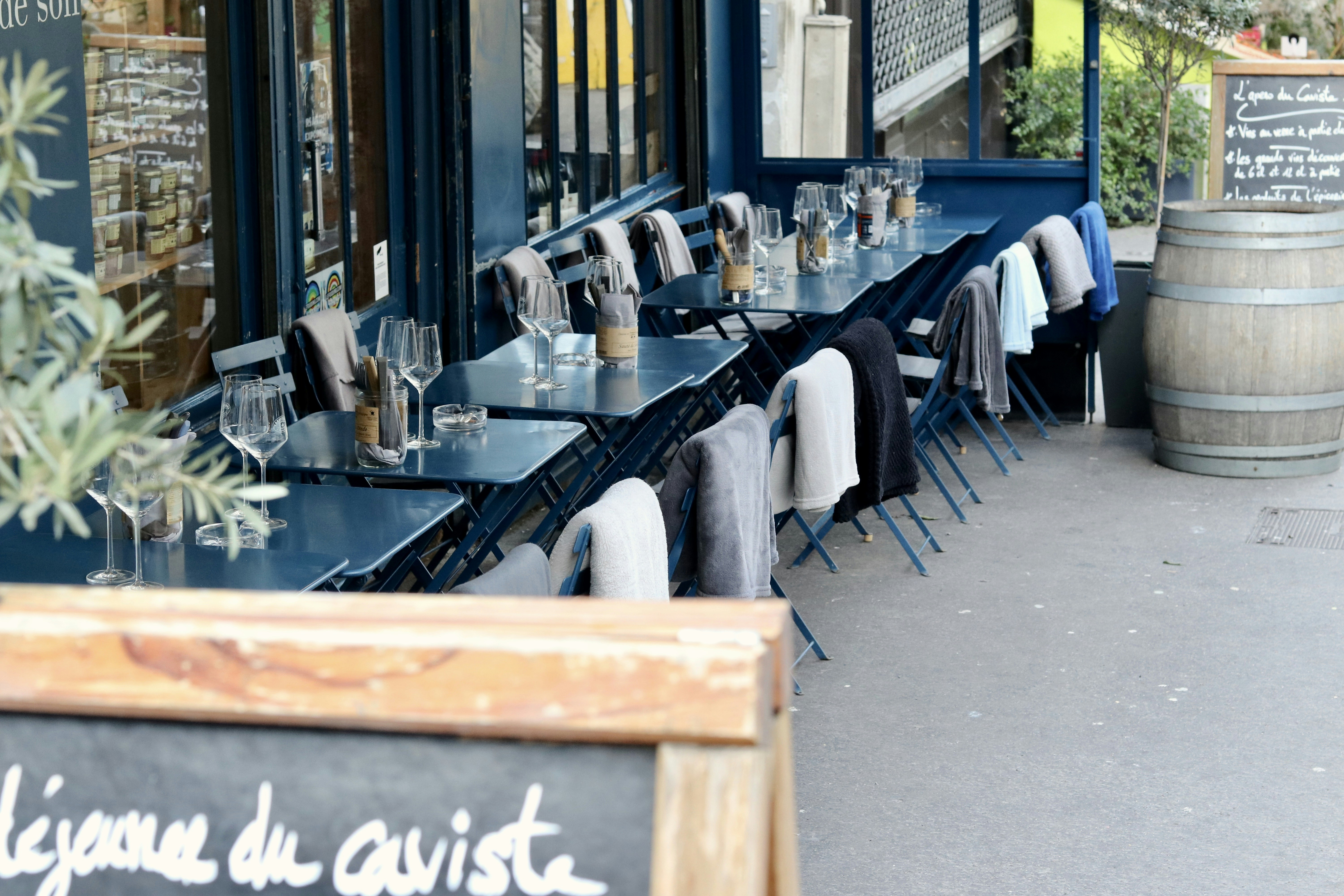 Row of blue tables and chairs with wine glasses and napkins outside a restaurant.