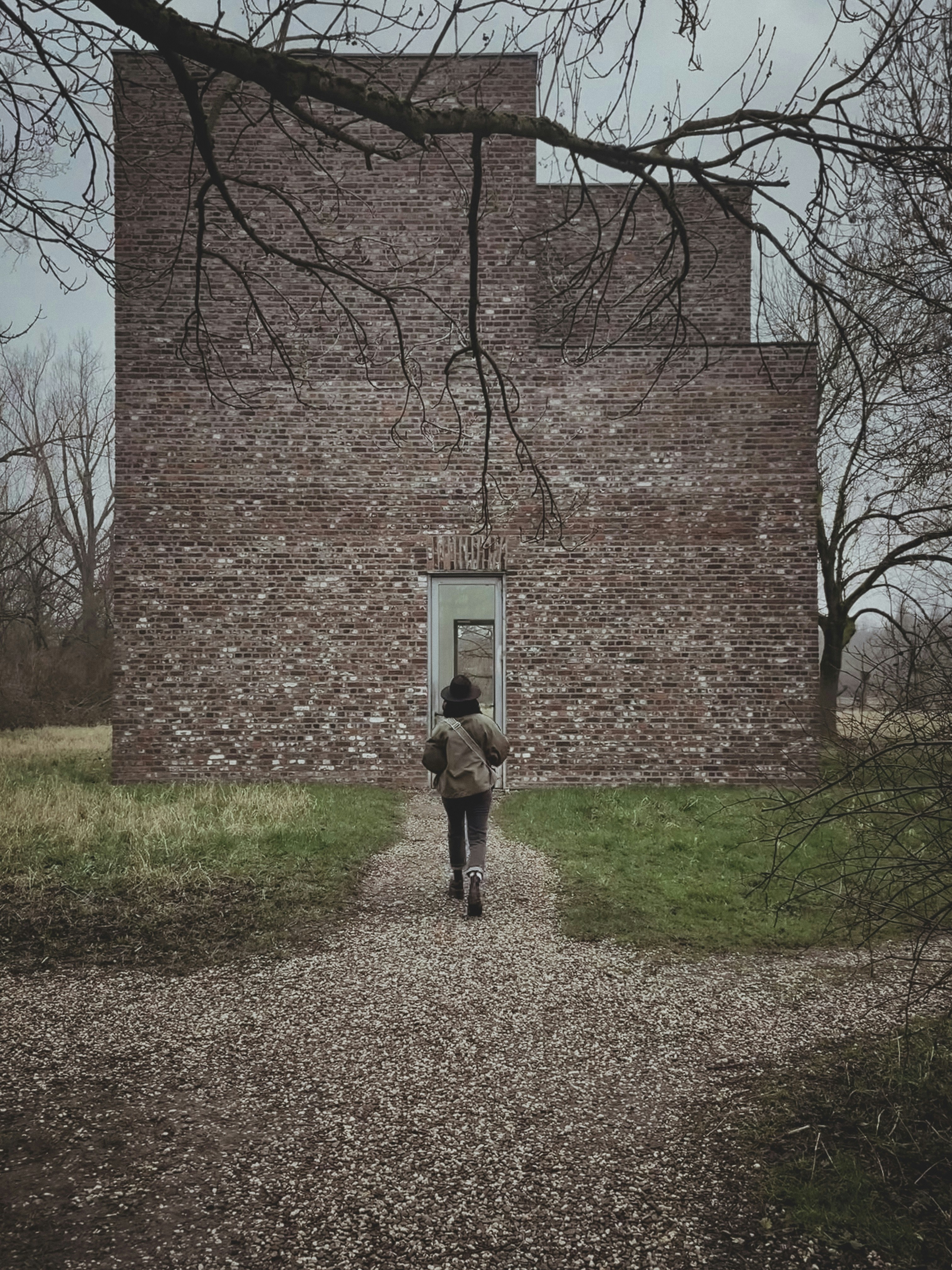 The Quiet Threshold: A lone figure approaches a brick doorway under bare branches