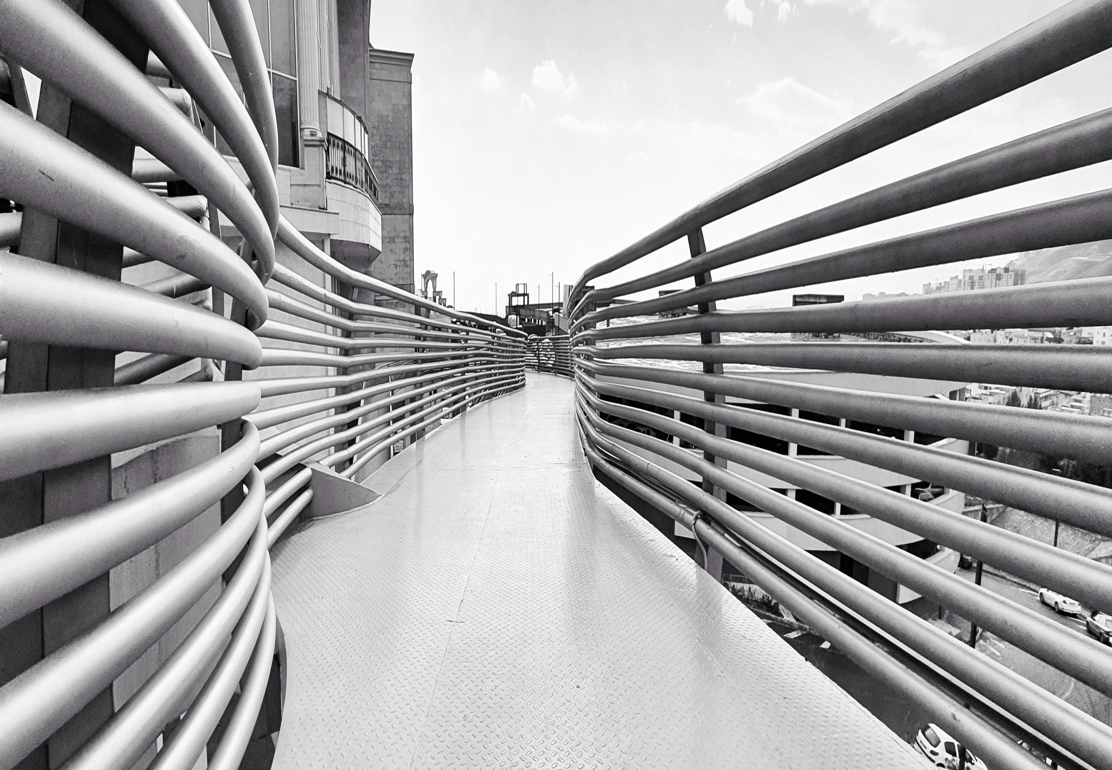 A sleek, curving walkway surrounded by metallic railings creates a dynamic perspective in a contemporary urban setting.
