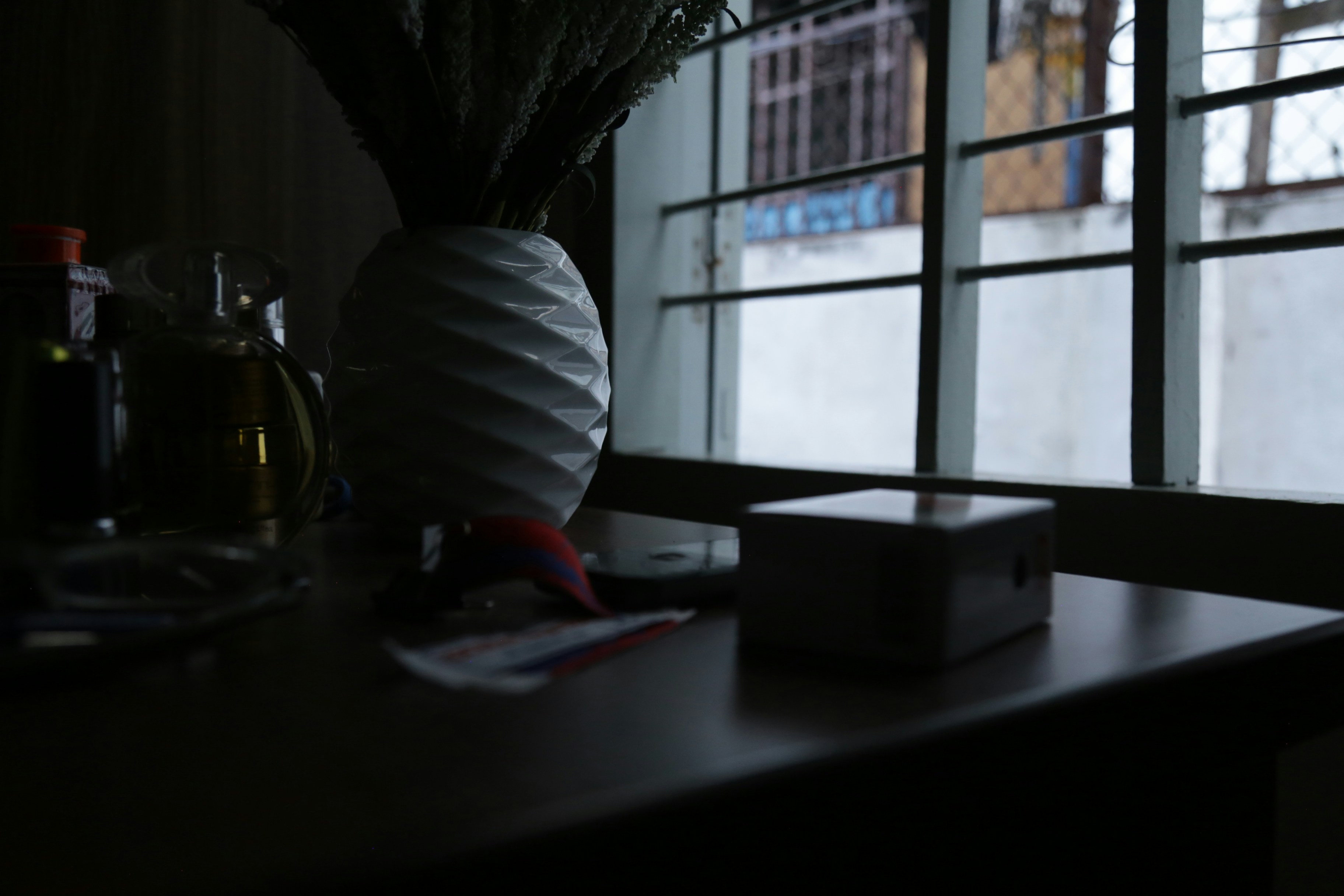 A softly lit interior scene featuring a textured vase with foliage, resting on a table beside a window. The muted colors enhance the tranquil atmosphere.