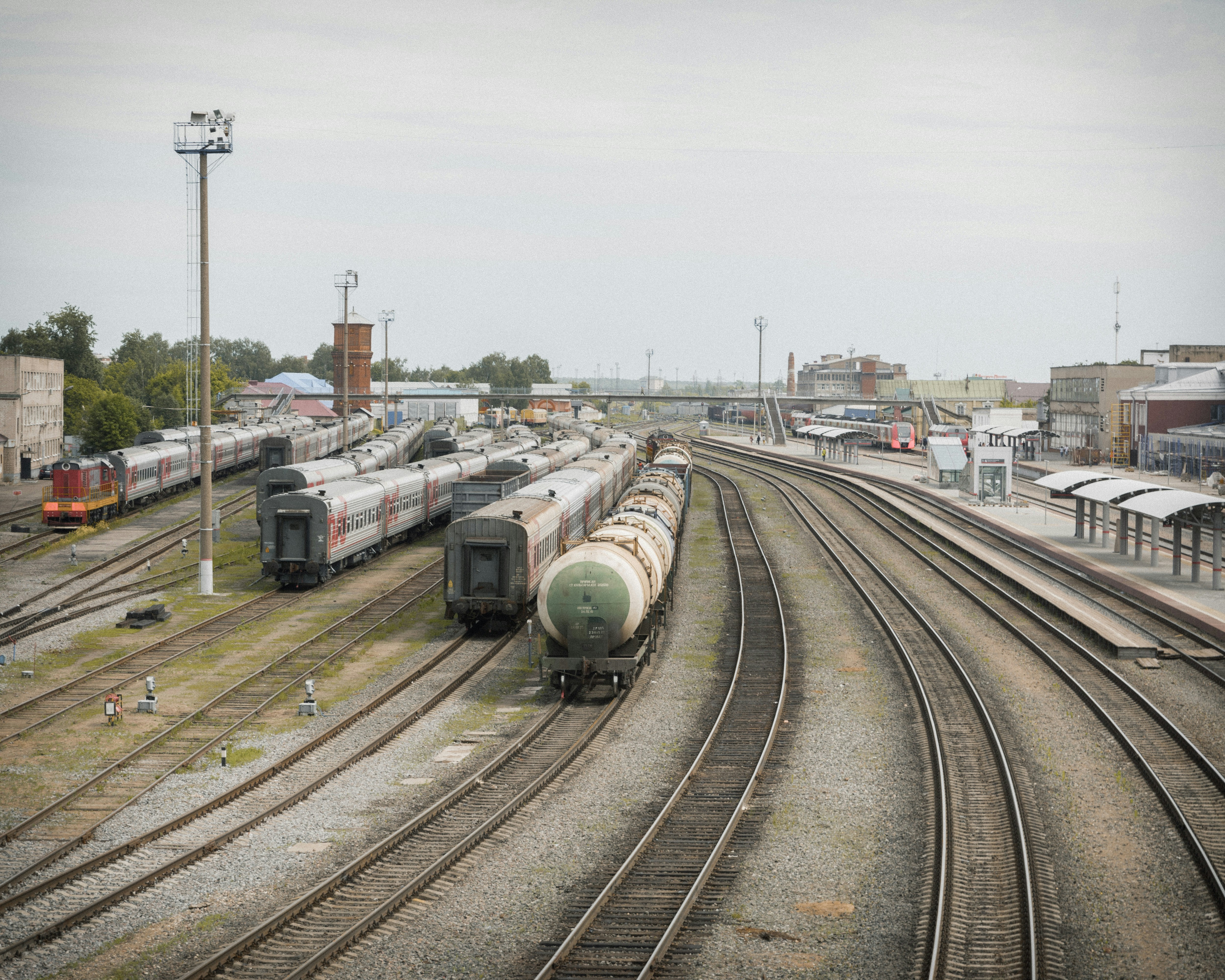 A railway yard bustling with various train cars, showcasing a blend of vintage and modern designs against a cloudy sky.