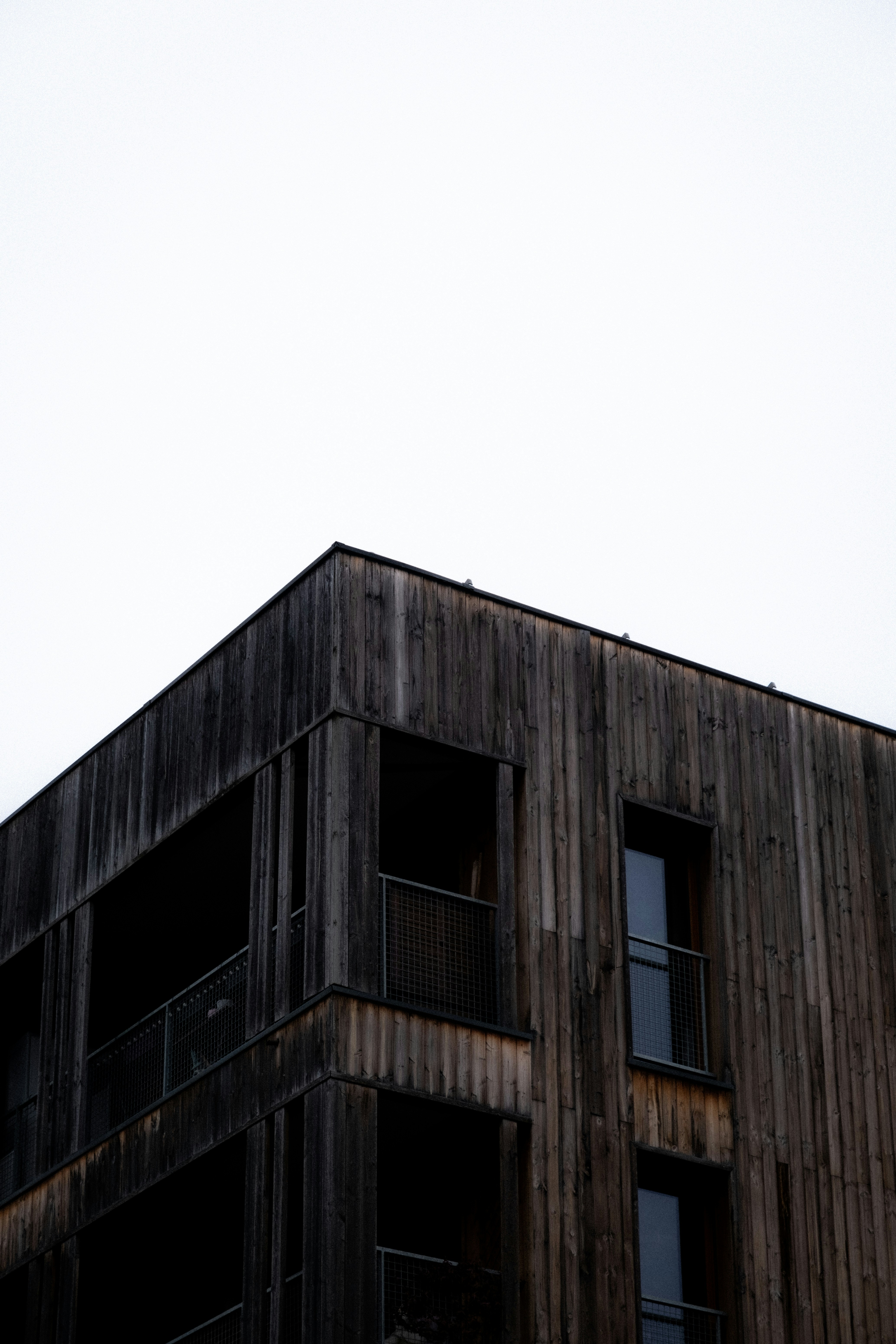 Cornered Facade: Weathered Timber Reaching into a Stark Sky