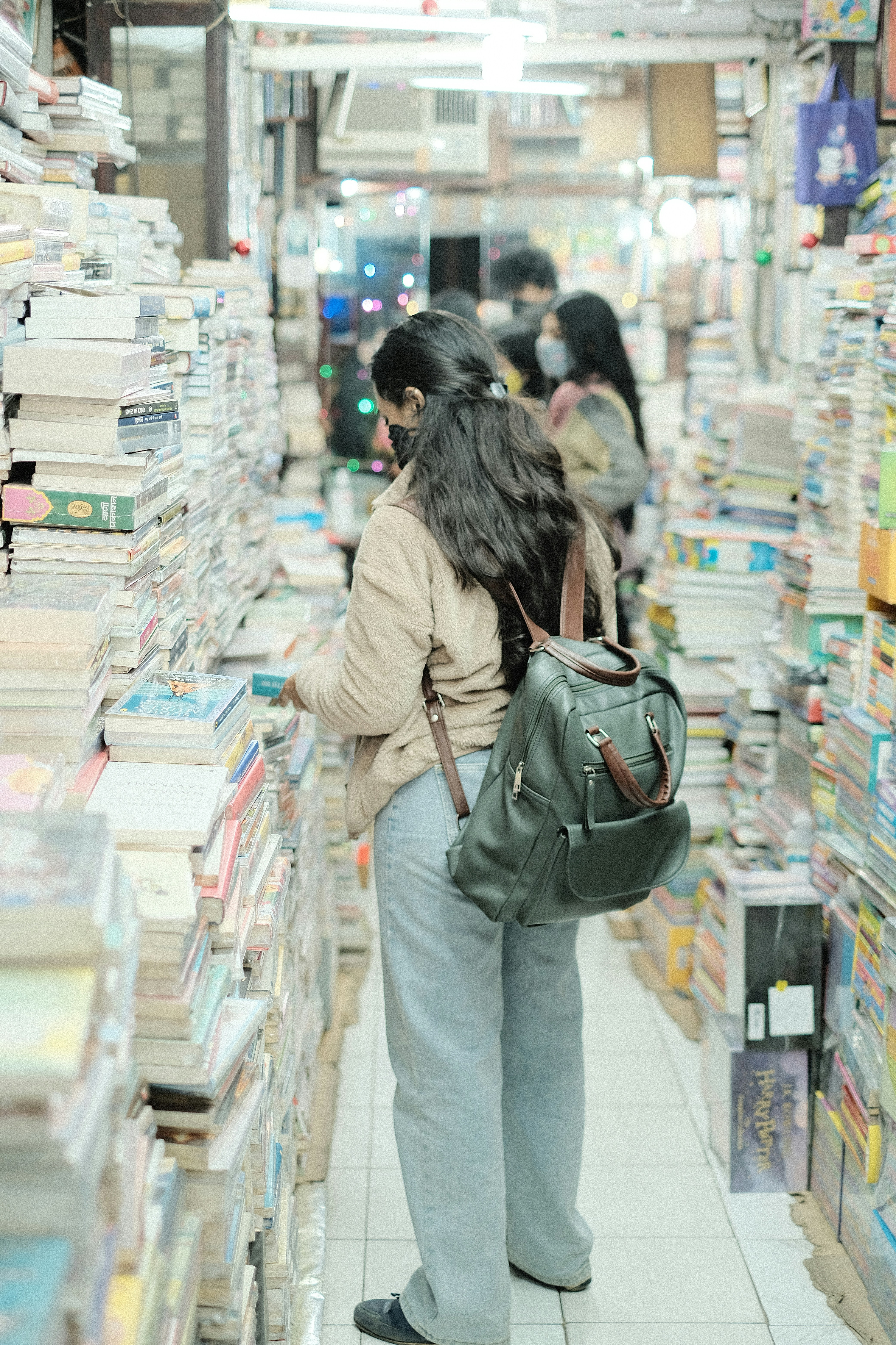 Individual browsing through towering stacks of books in a cozy bookstore filled with vibrant titles and warm lighting.