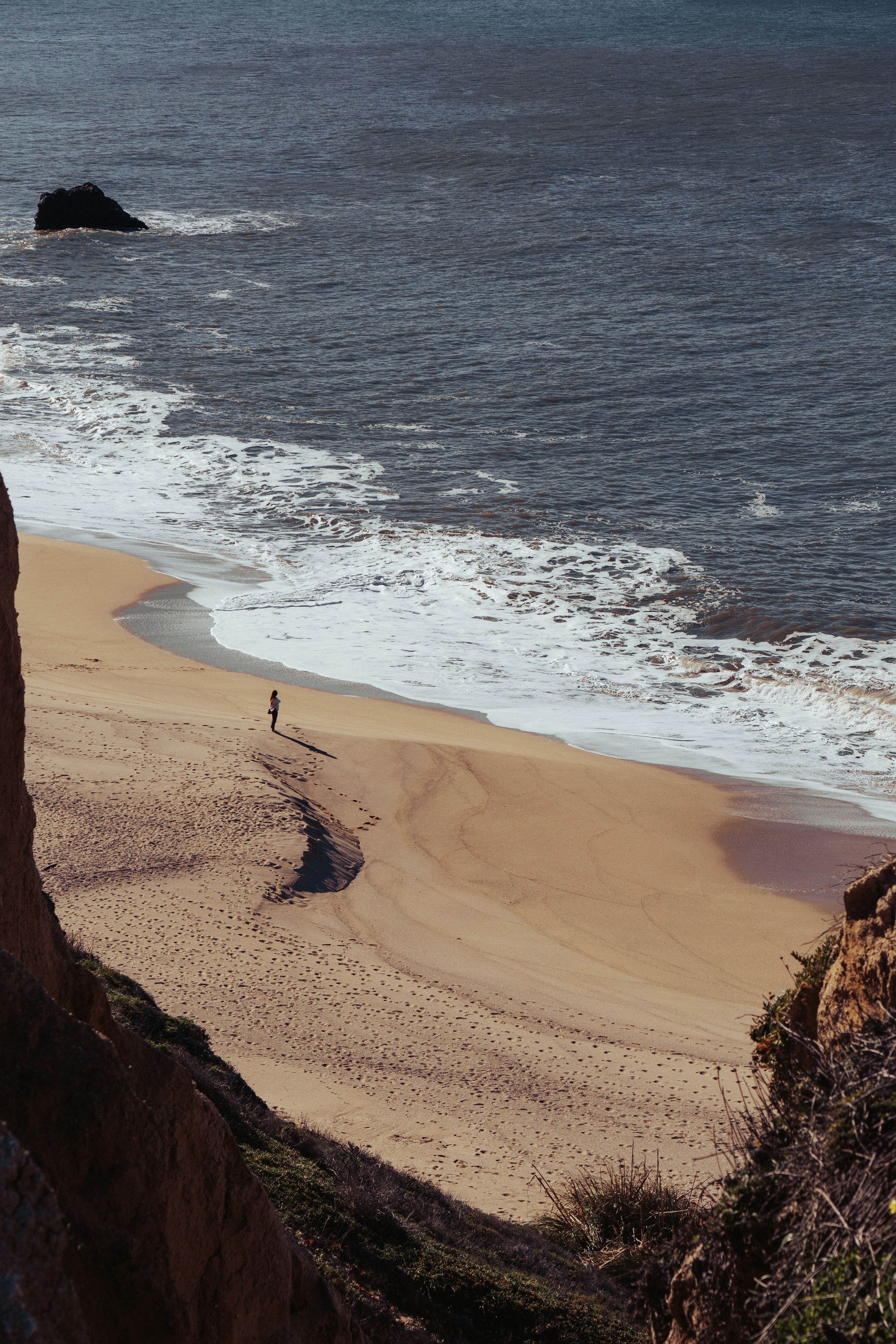 A lone figure stands on a sandy beach, surrounded by gentle waves and rocky outcrops, capturing the essence of tranquility and isolation.