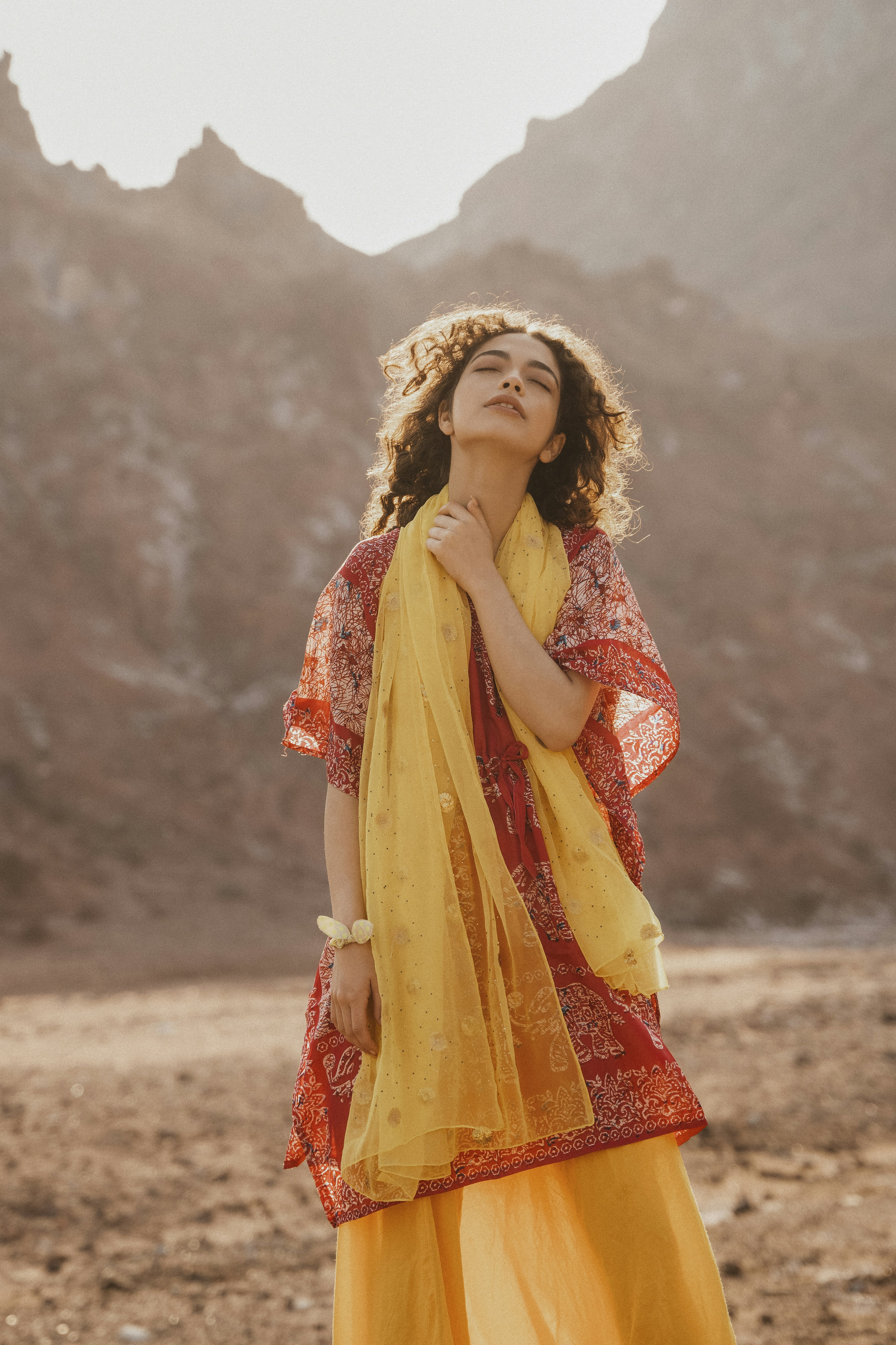 Woman in vibrant attire stands against a rugged landscape, exuding confidence and grace. The flowing fabrics and natural backdrop create a harmonious blend.