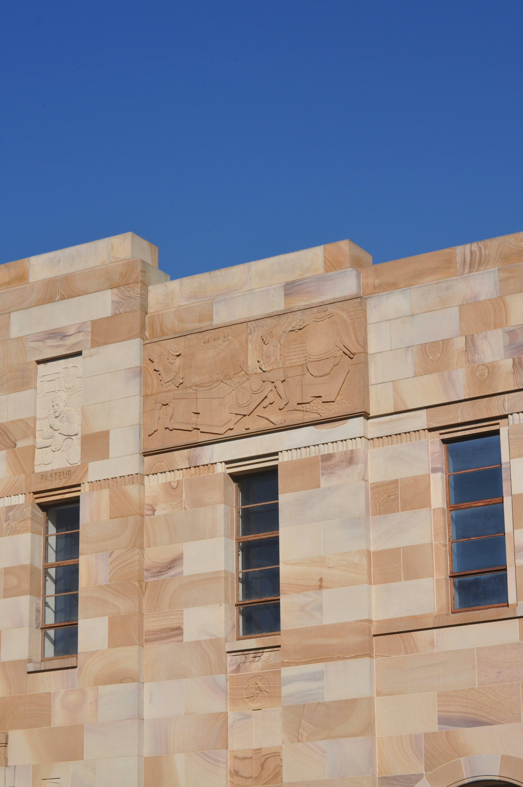 Intricate stone carvings adorn the facade of a building, showcasing historical figures and scenes against a clear blue sky.