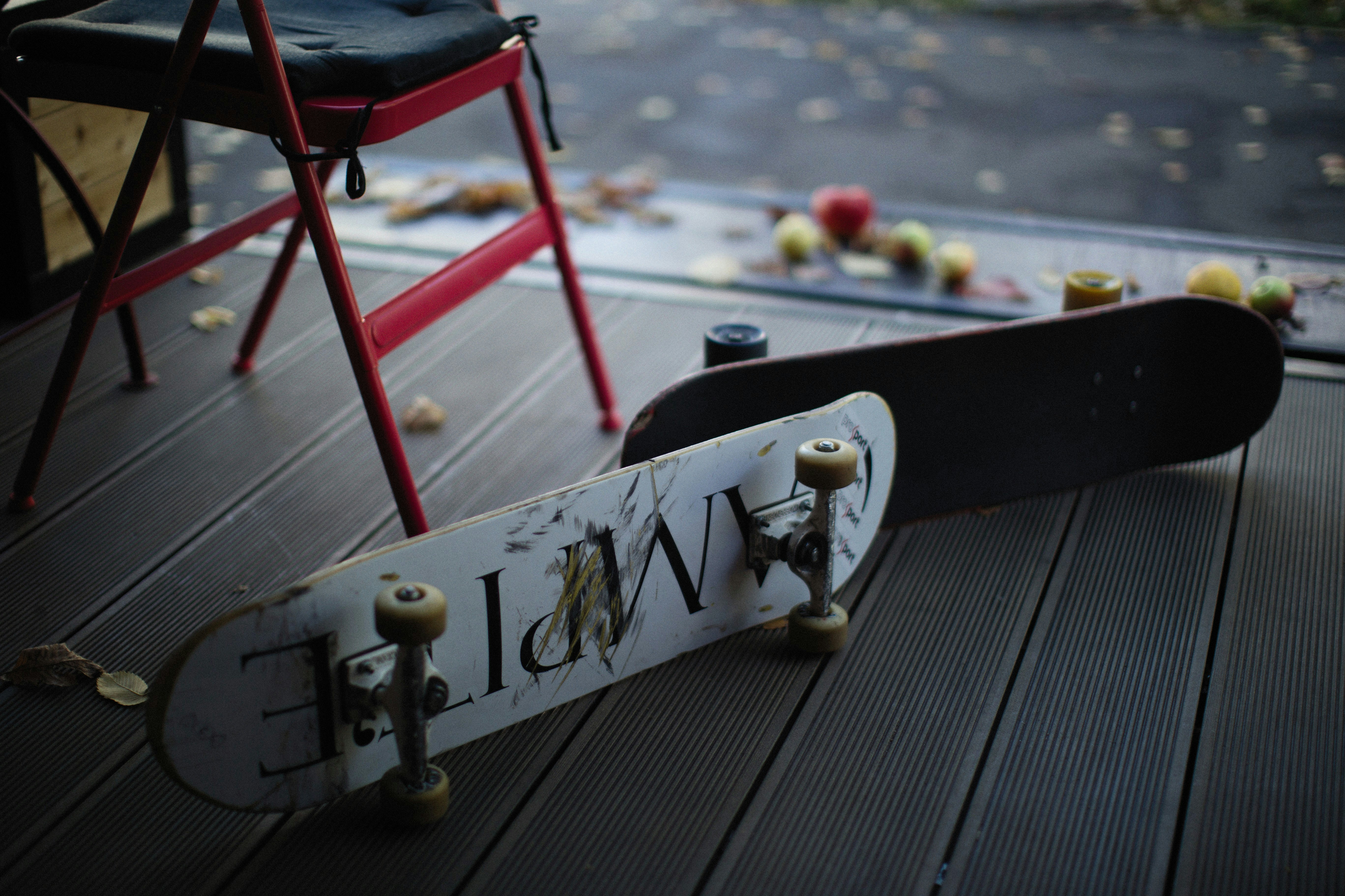Two skateboards resting on a textured surface, surrounded by scattered apples and a red chair in the background.