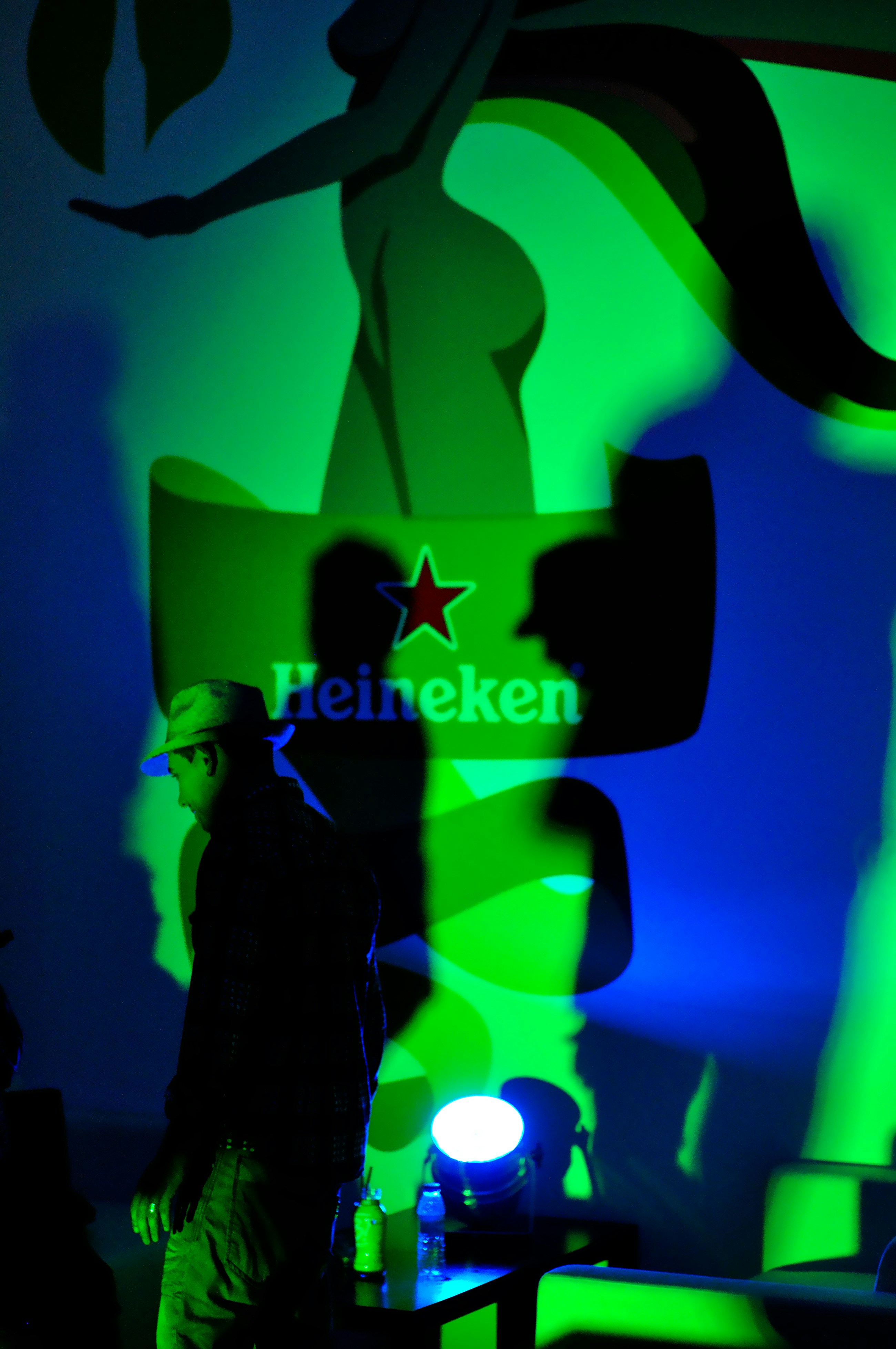 Neon-green Silhouettes Beside a Heineken Banner in a Dim Lounge