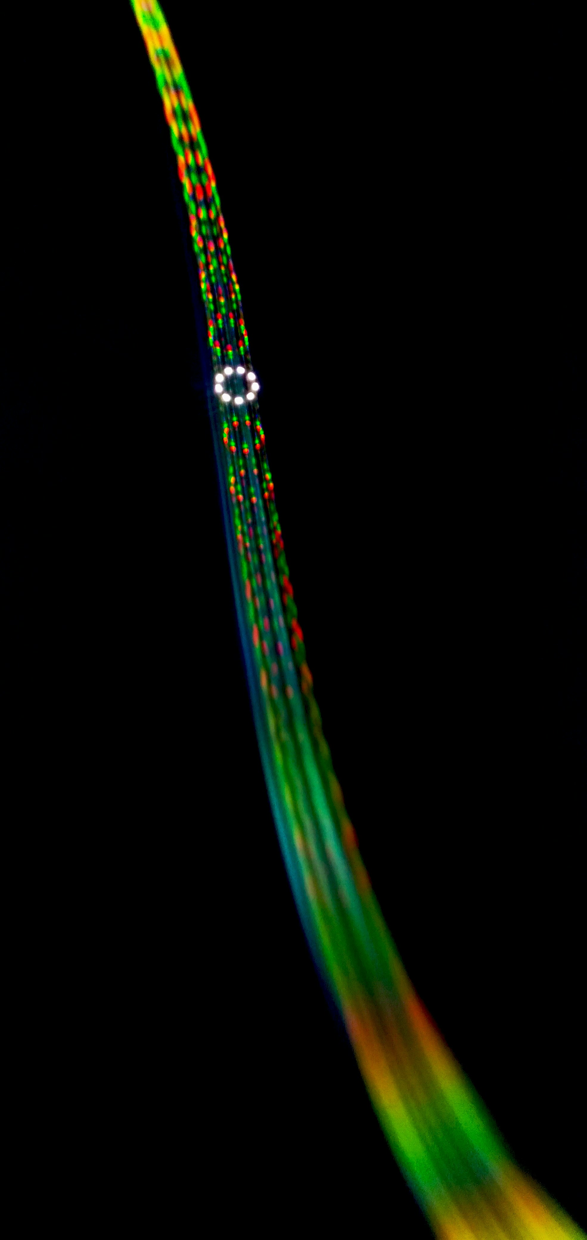 A close-up of a curved string of multicolor LEDs against a black background, featuring a bright circular bokeh cluster.