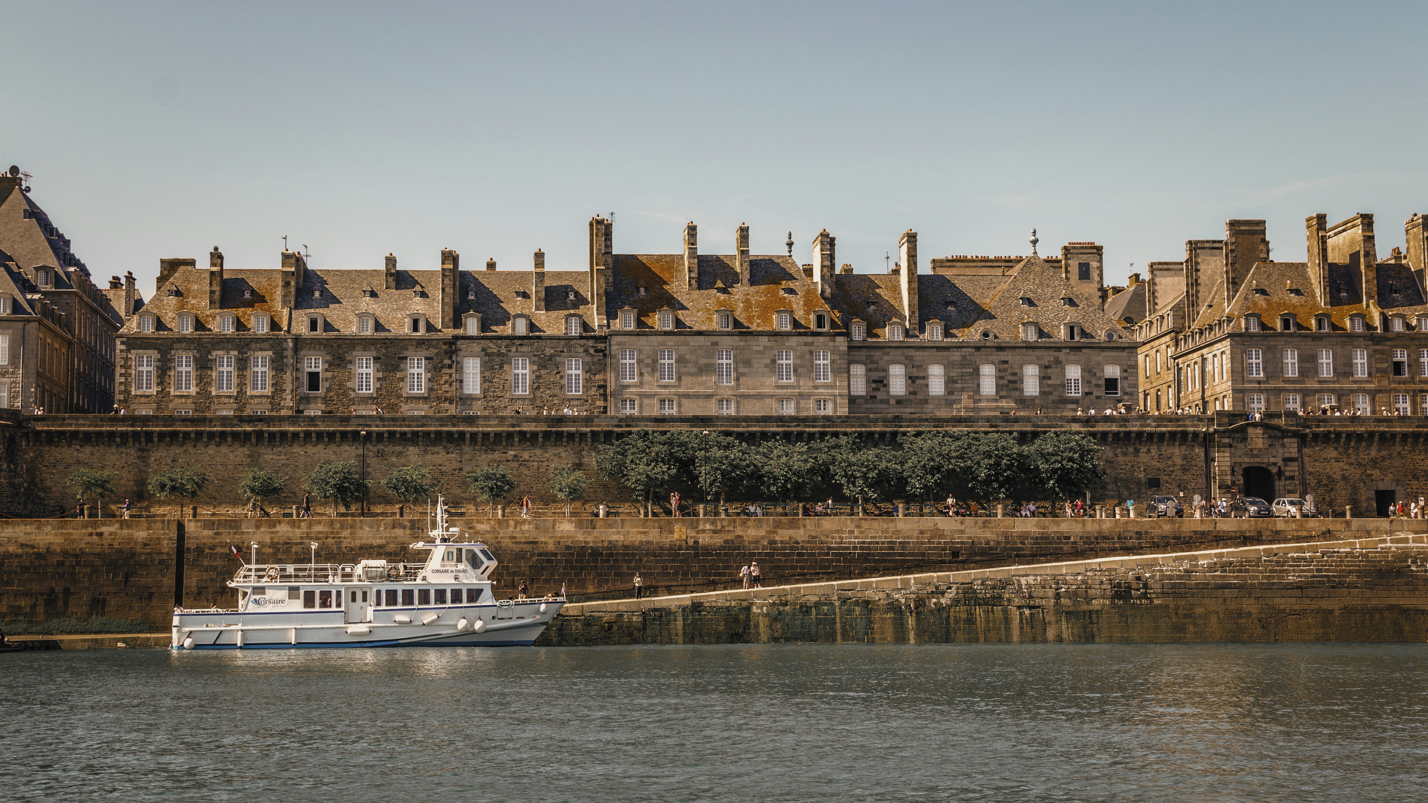Boat moored next to a stone pier with historic buildings in the background under a clear sky.