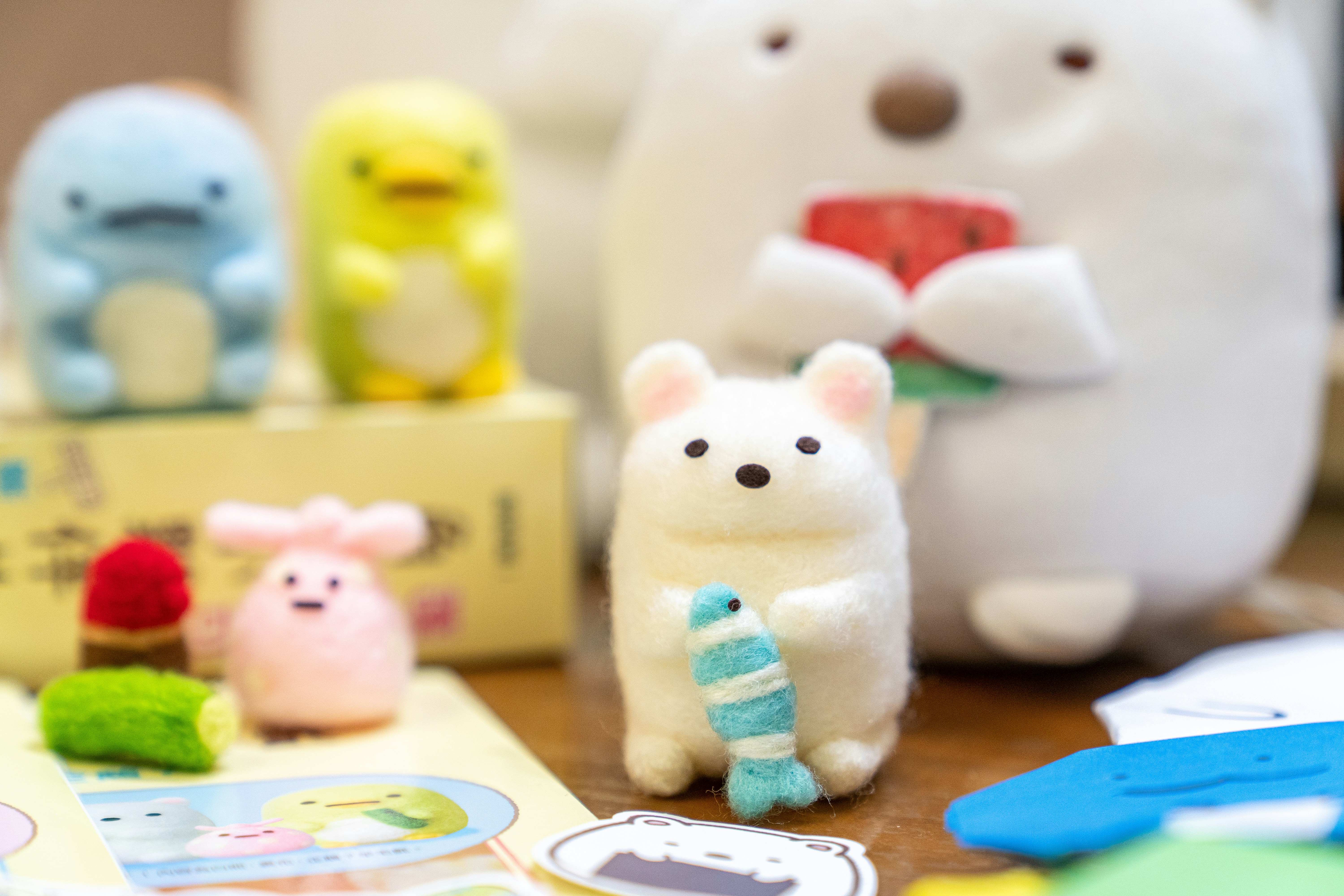A collection of adorable felted characters, featuring a white bear holding a striped fish, surrounded by colorful plush toys and playful stationery.
