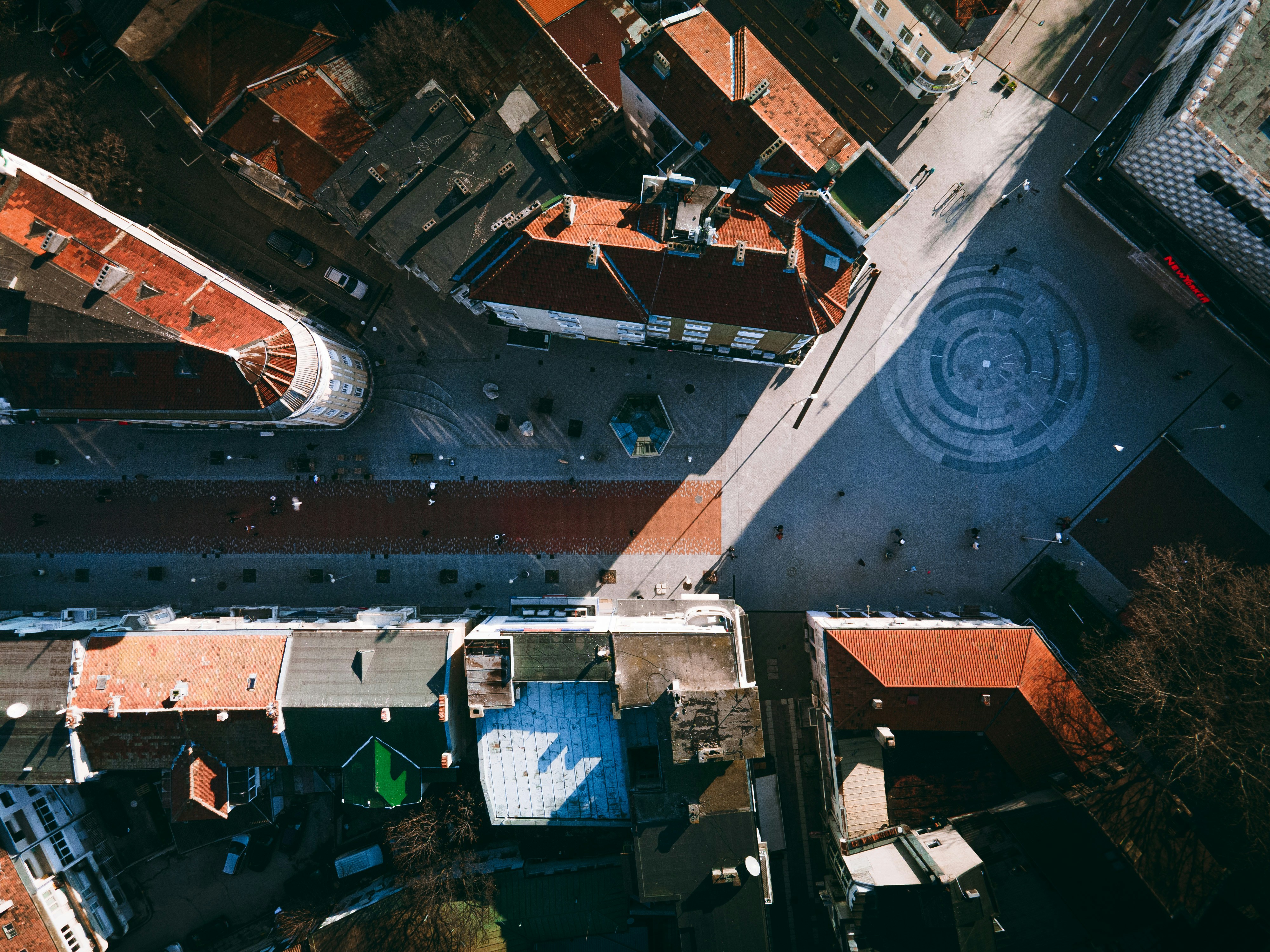 Aerial view capturing the intricate layout of city streets and rooftops, emphasizing the contrast between light and shadow. The circular plaza serves as a focal point amidst the surrounding architecture.