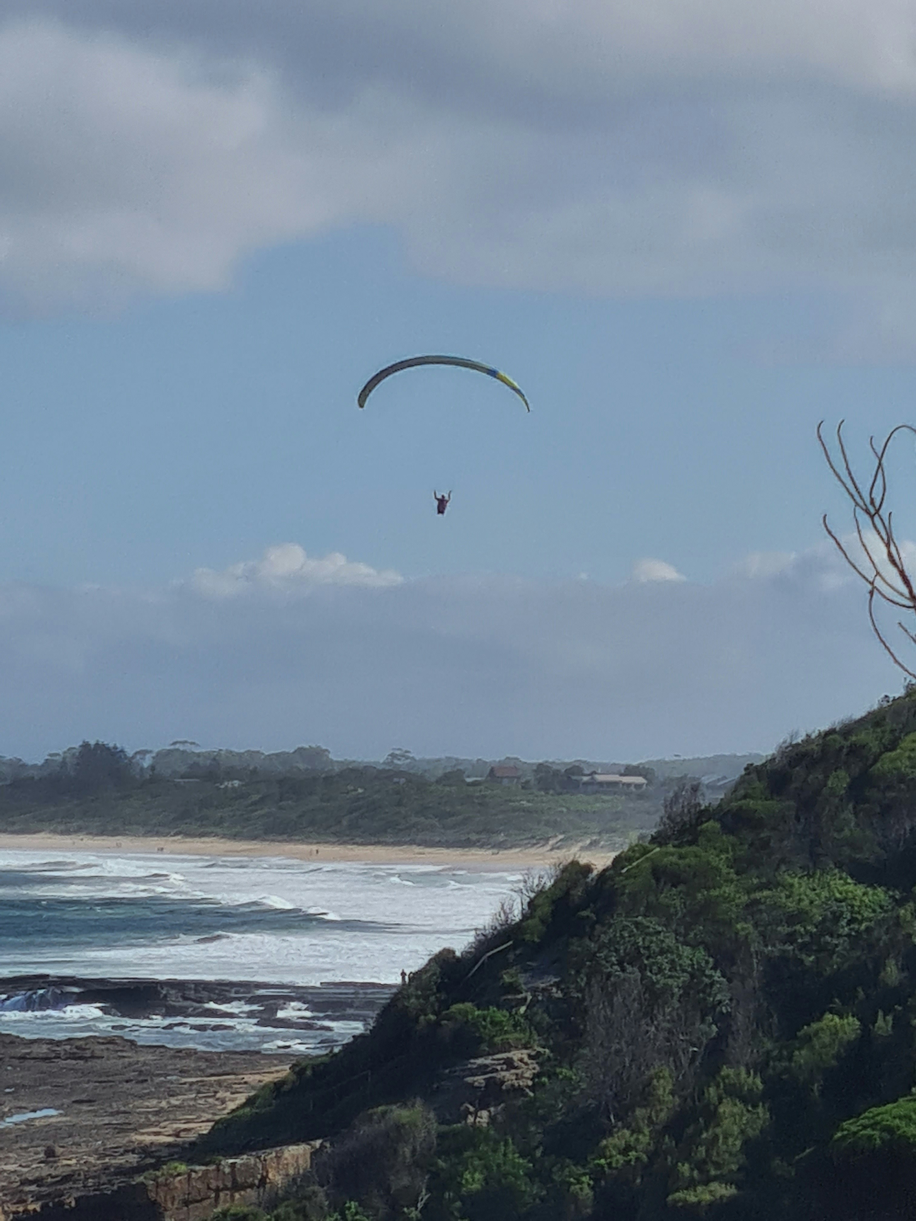 a paraglider is flying over the ocean on a cloudy day