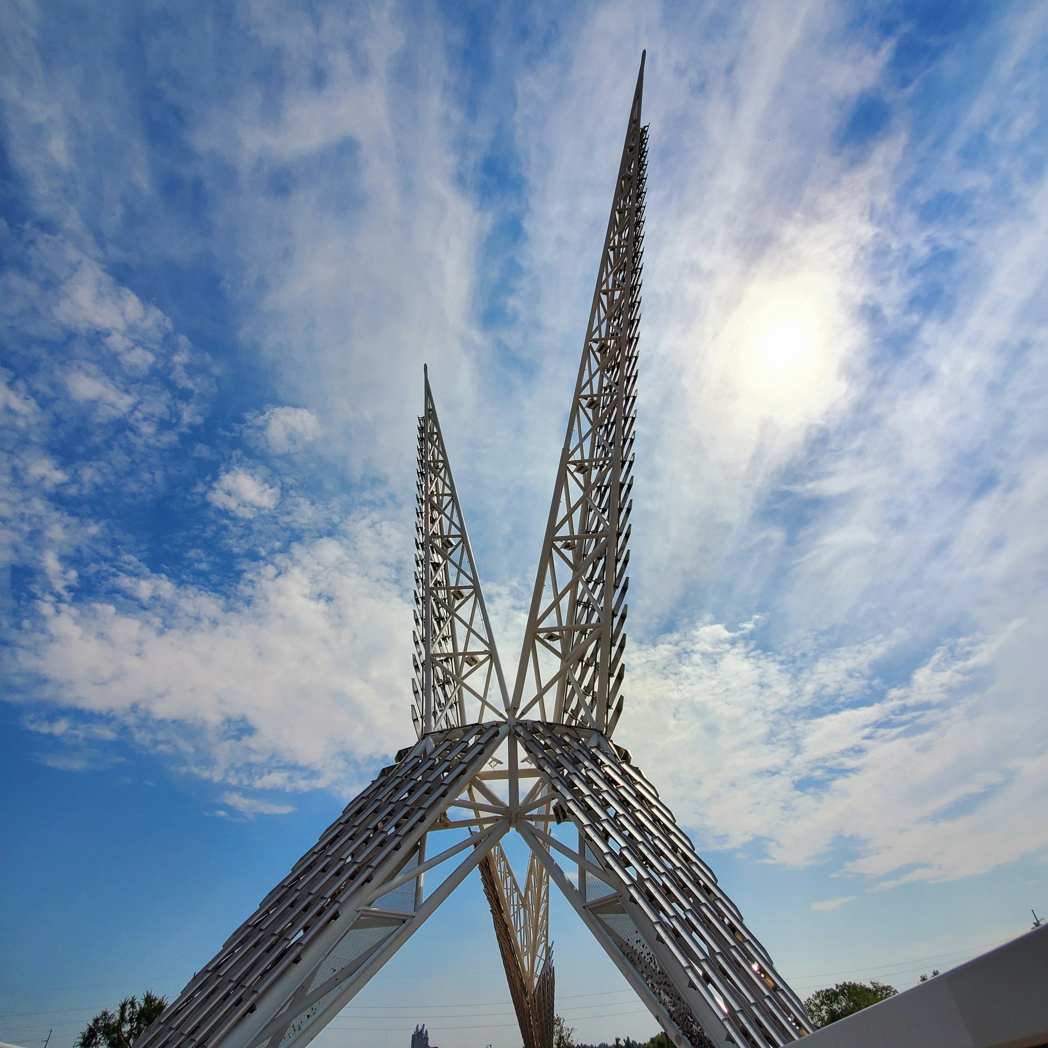 Striking architectural structure with sharp, soaring spires against a backdrop of dynamic clouds and sunlight.