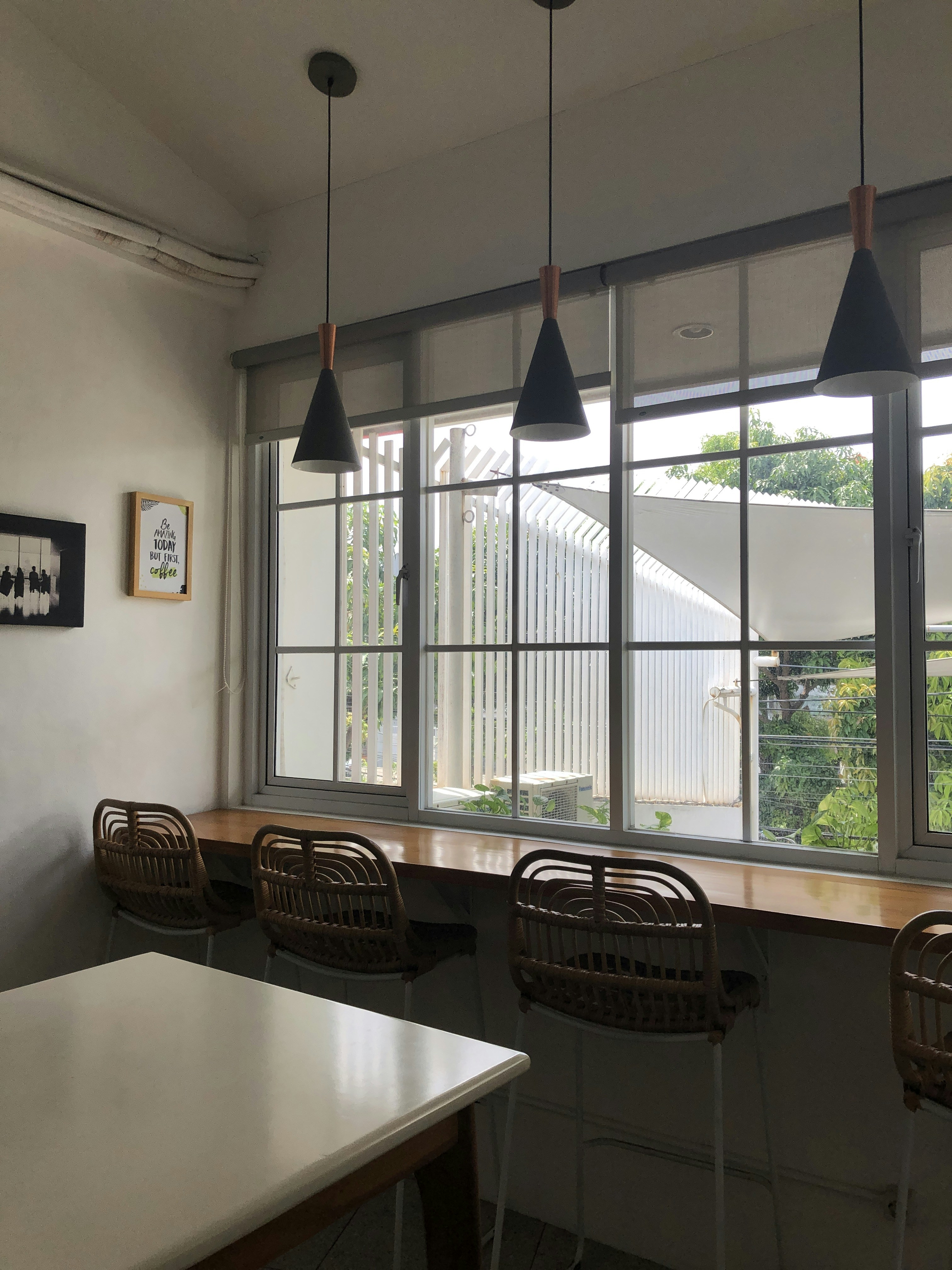 Modern café interior featuring sleek pendant lights and a wooden countertop overlooking greenery through large windows.