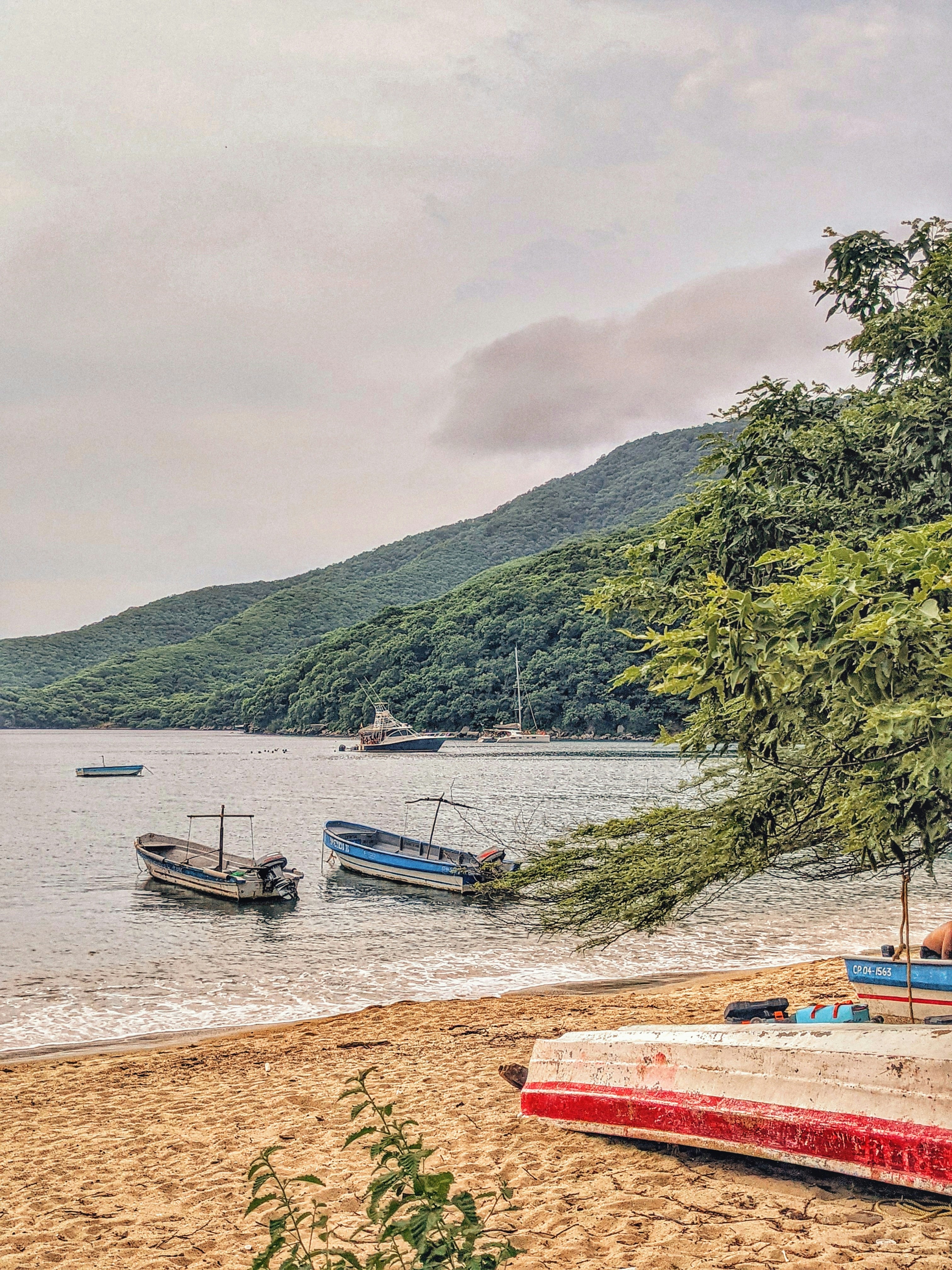 Fishing boats anchored in a tranquil bay, framed by lush green hills and a sandy beach. The scene evokes a sense of peaceful seaside escape.