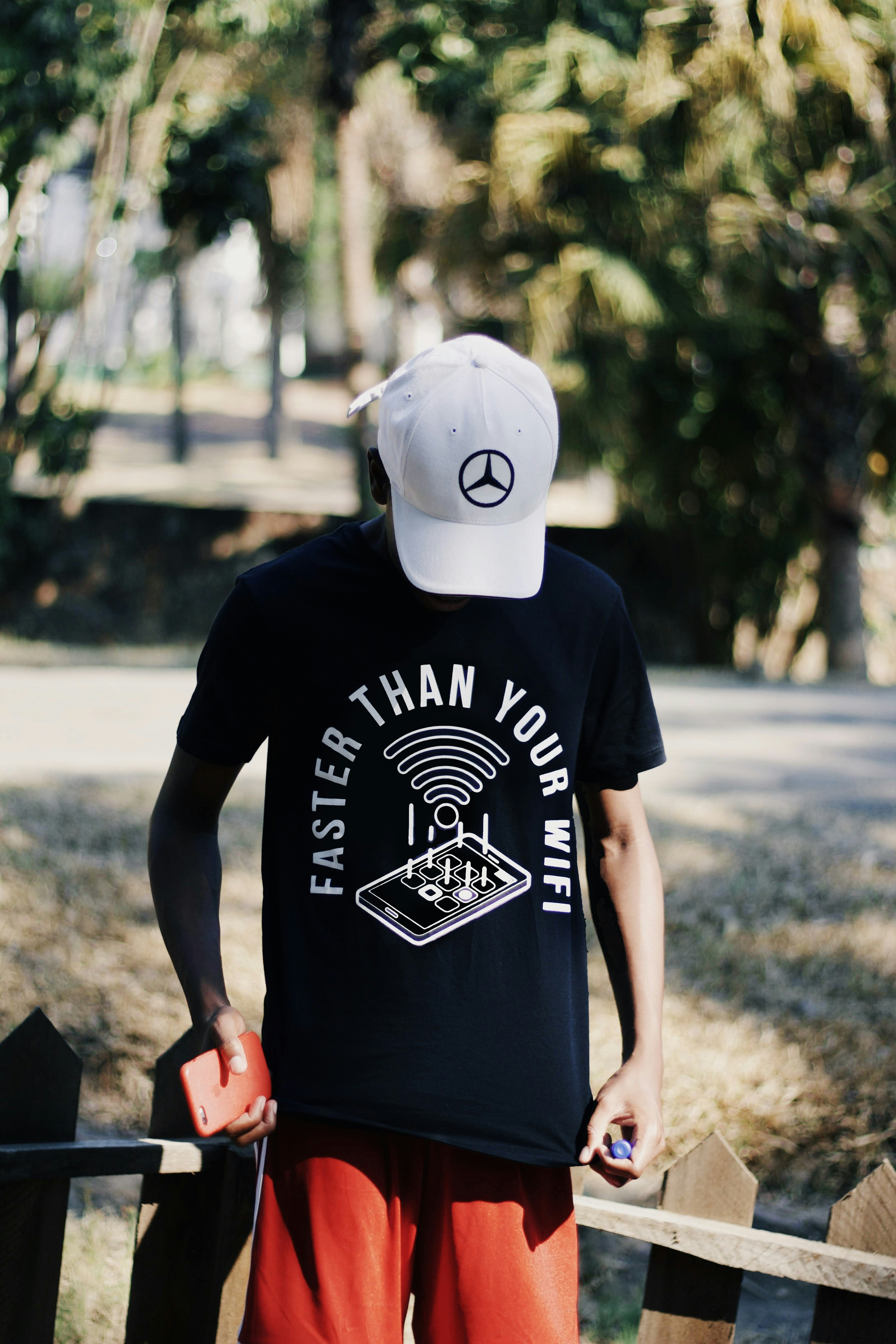 Individual wearing a black t-shirt with a humorous WiFi graphic stands in a sunlit outdoor setting, holding a smartphone. The scene captures a lighthearted moment about modern technology.