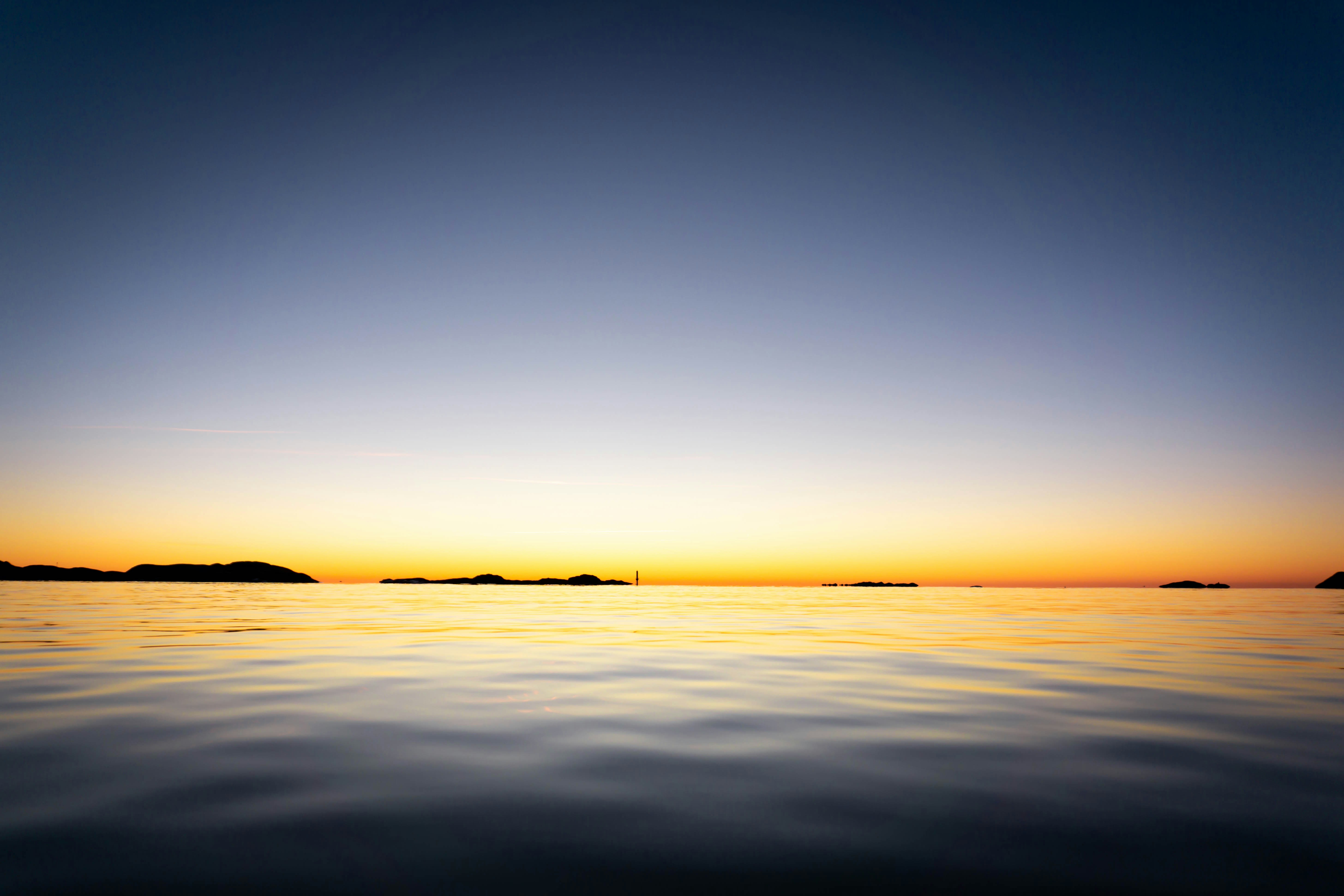 Serene sunset over a tranquil sea with a gradient sky transitioning from deep blue to warm orange hues.