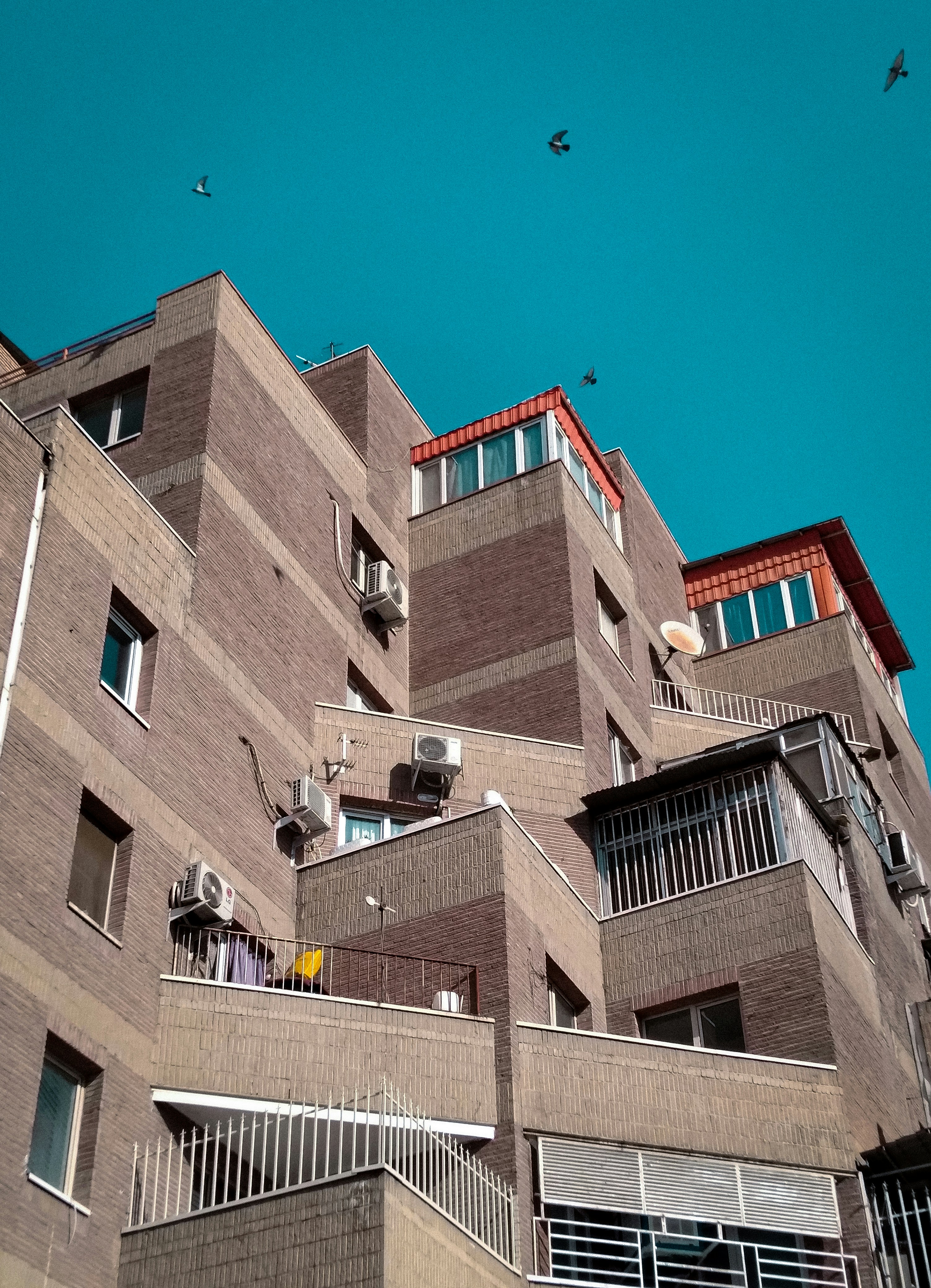 A modern apartment building with a unique angular design, featuring air conditioning units and balconies under a clear blue sky.