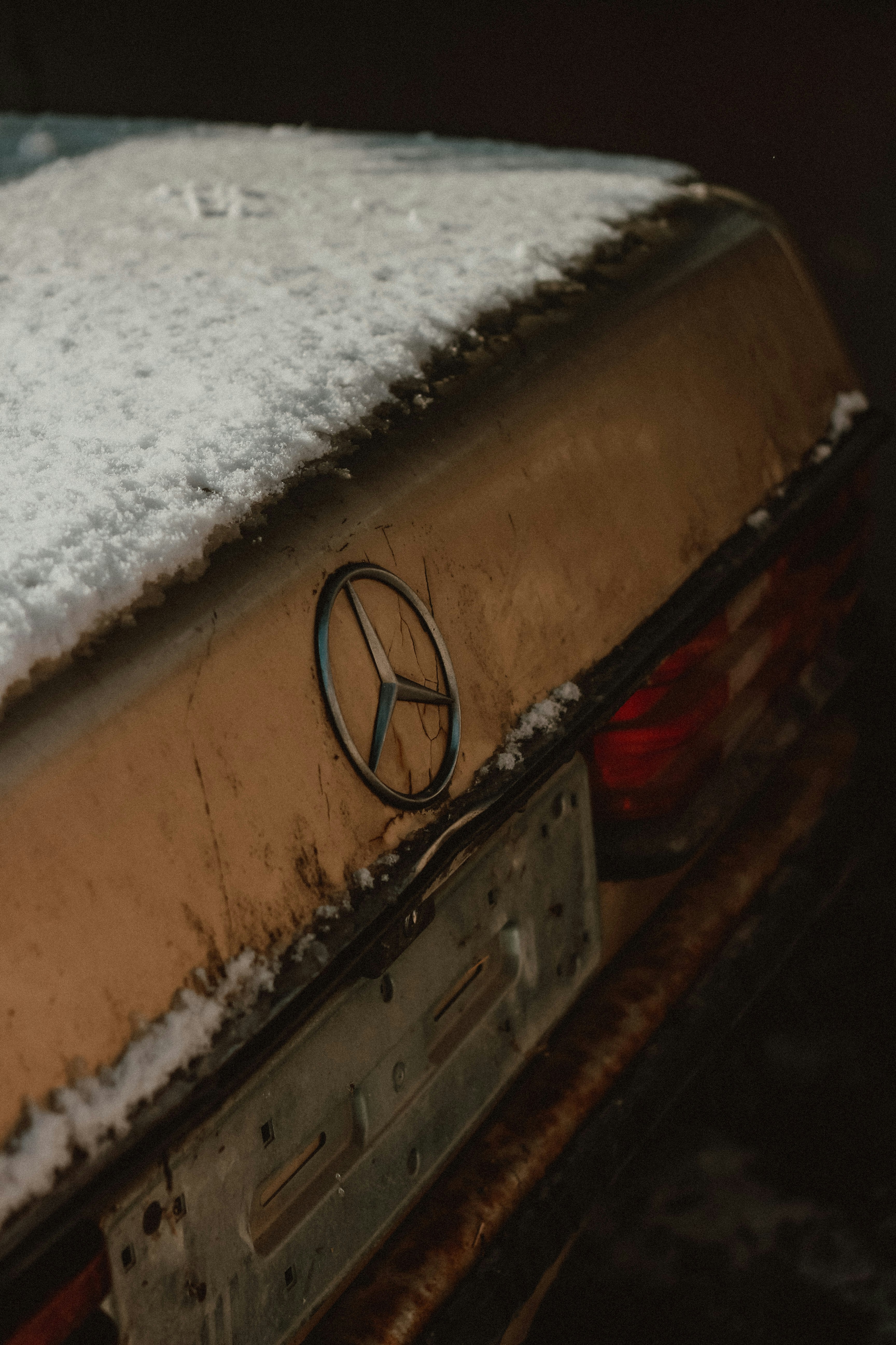 Snow-covered Mercedes emblem on a vintage car, showcasing the contrast between decay and timeless design.