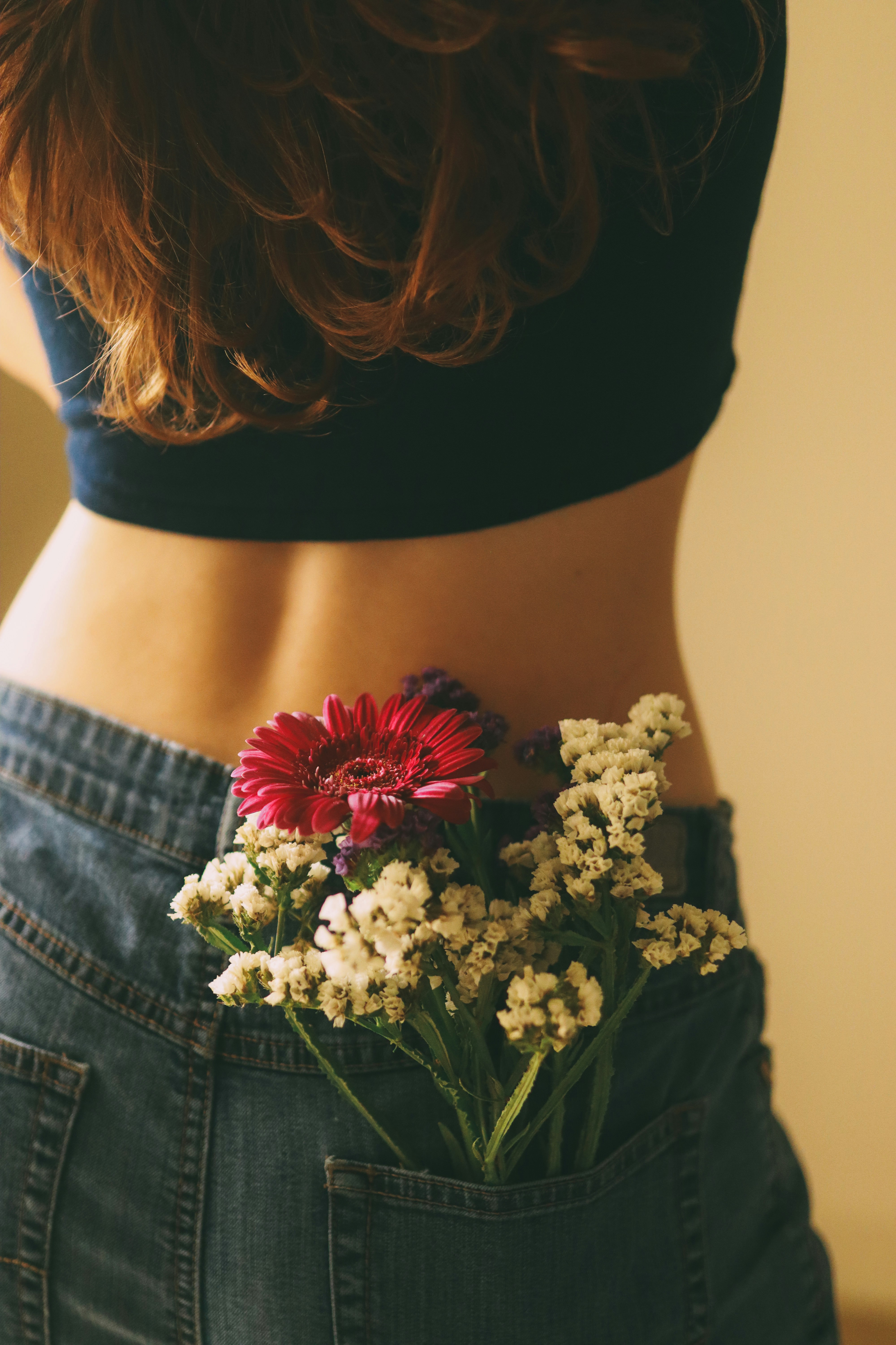 A woman's back showcases a playful arrangement of colorful flowers peeking from her denim pocket, blending fashion with nature's beauty.