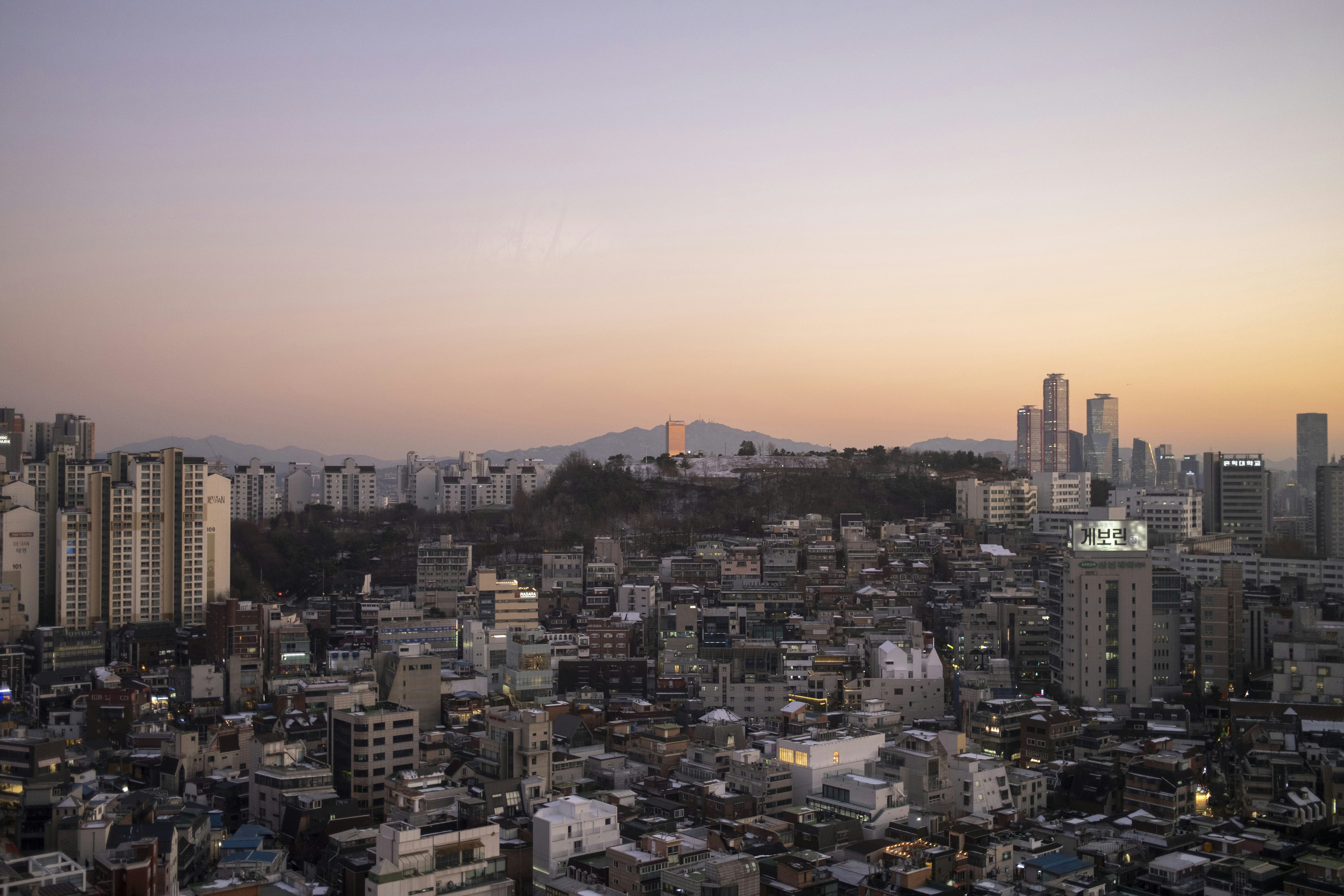 Cityscape with high-rise buildings set against a backdrop of distant mountains at sunset.
