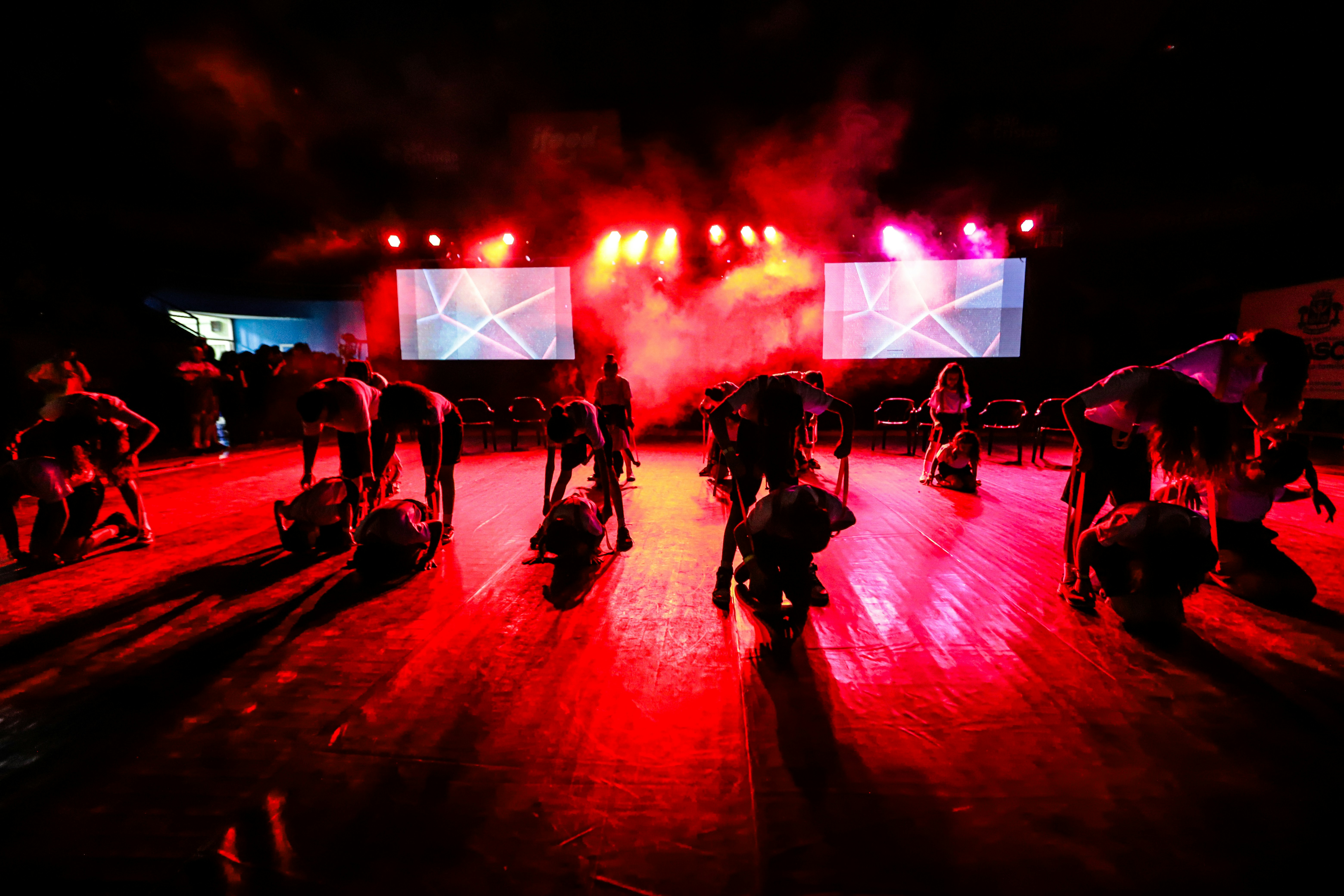 Dancers in dynamic poses silhouetted against vibrant red stage lights, creating a striking contrast with the dark surroundings.